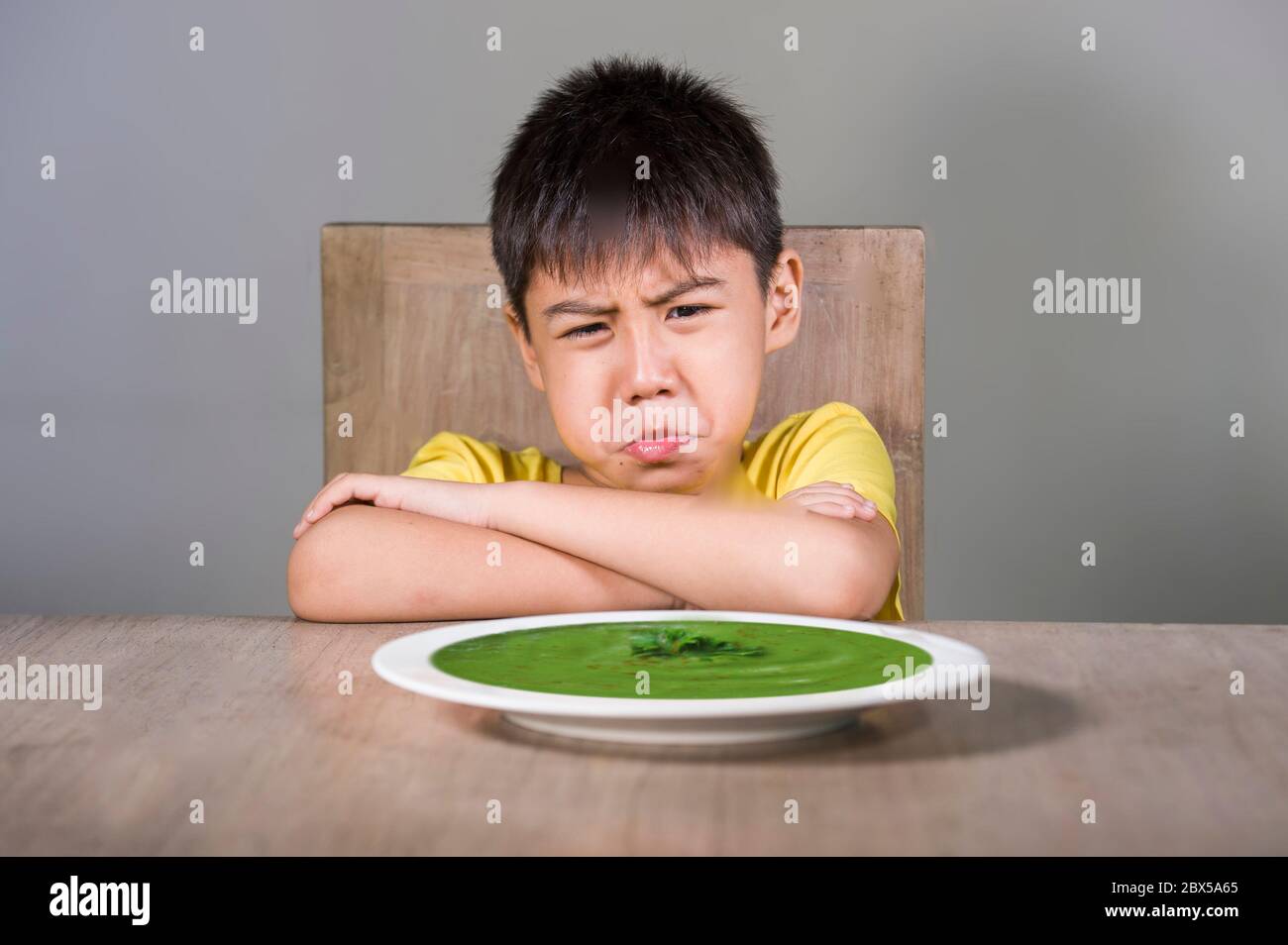 7 or 8 years old upset and disgusted Asian kid sitting on table ...