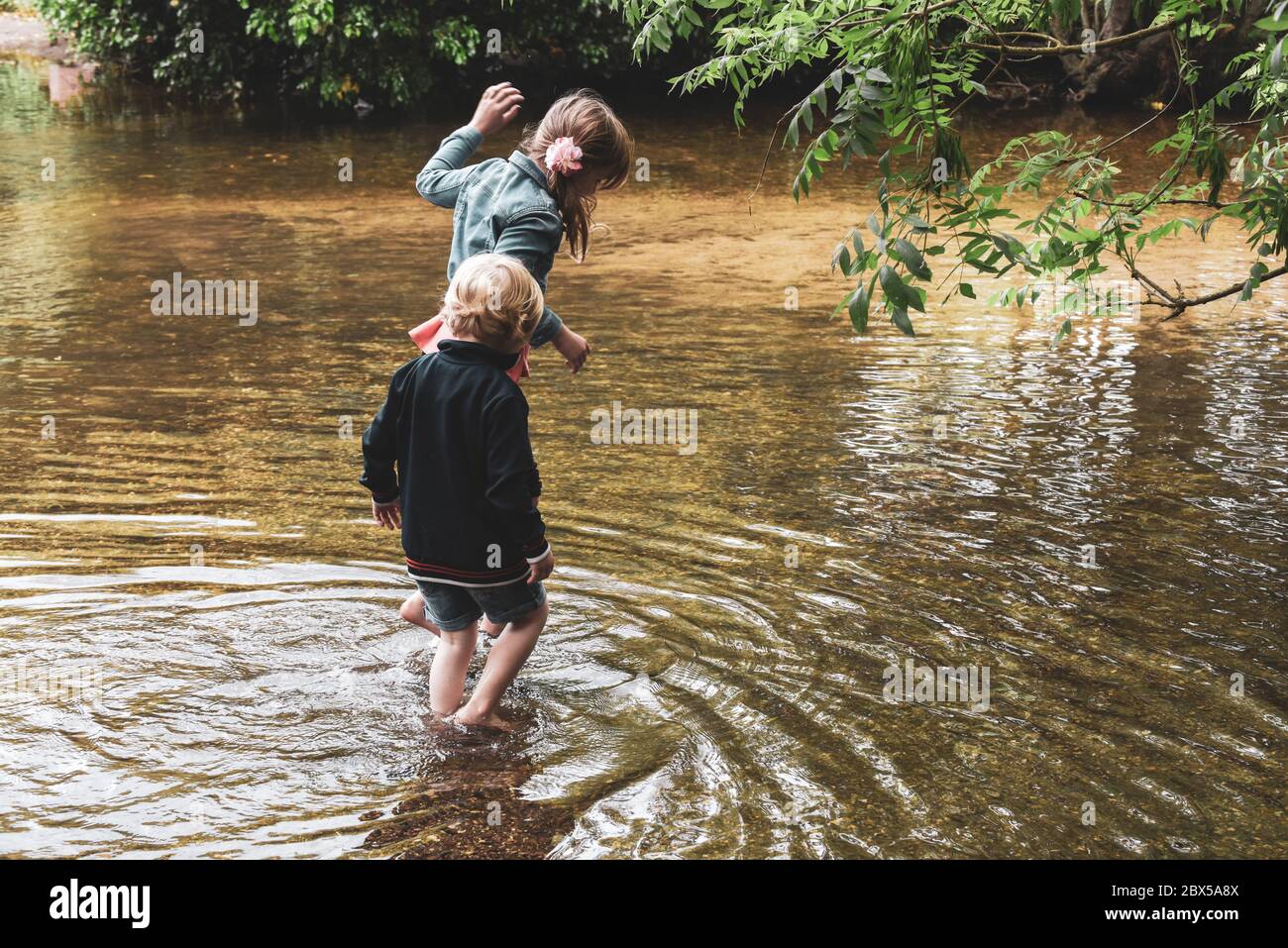 Children playing outside in a shallow stream paddling in the water ...