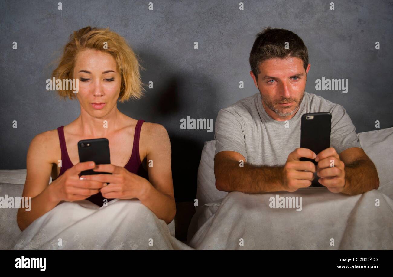 young attractive couple using mobile phone in bed ignoring and ...