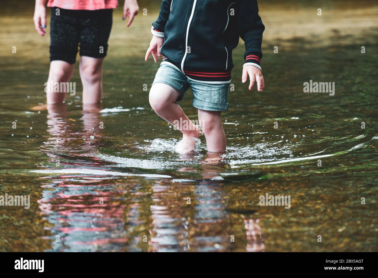Children paddle in a stream of water outside during a sunny day out ...