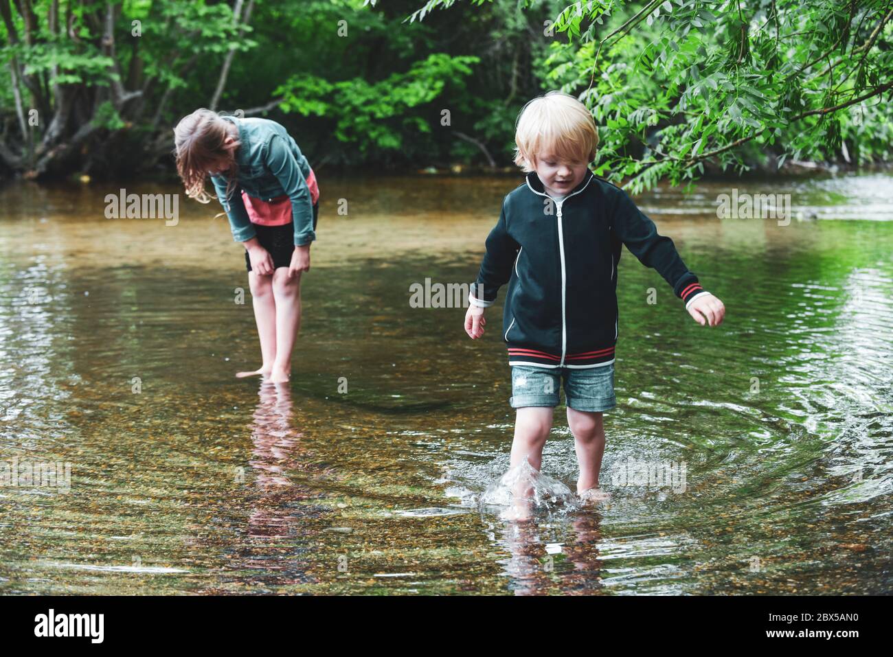 Children paddle in a stream of water outside during a sunny day out ...