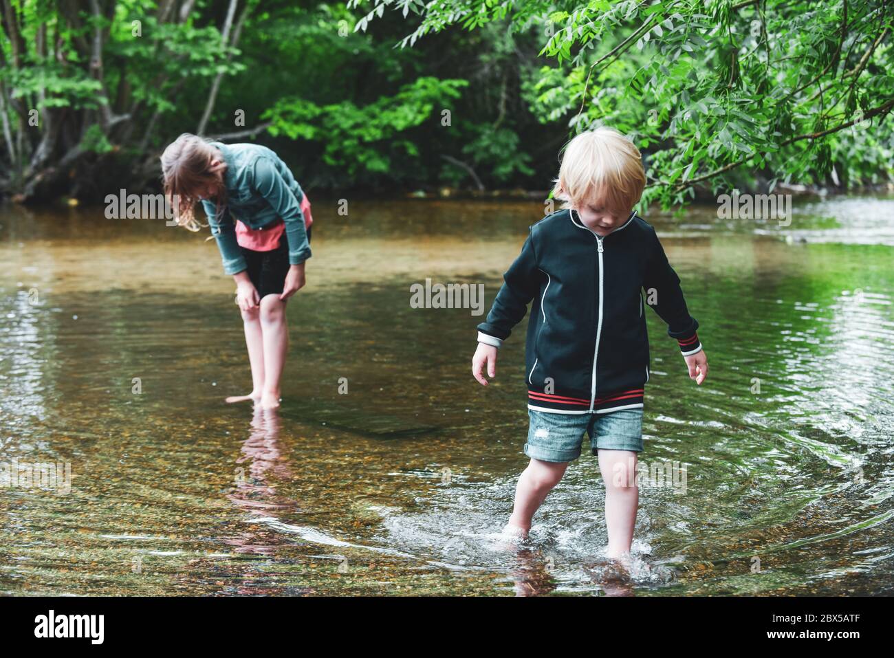 Children paddle in a stream of water outside during a sunny day out ...