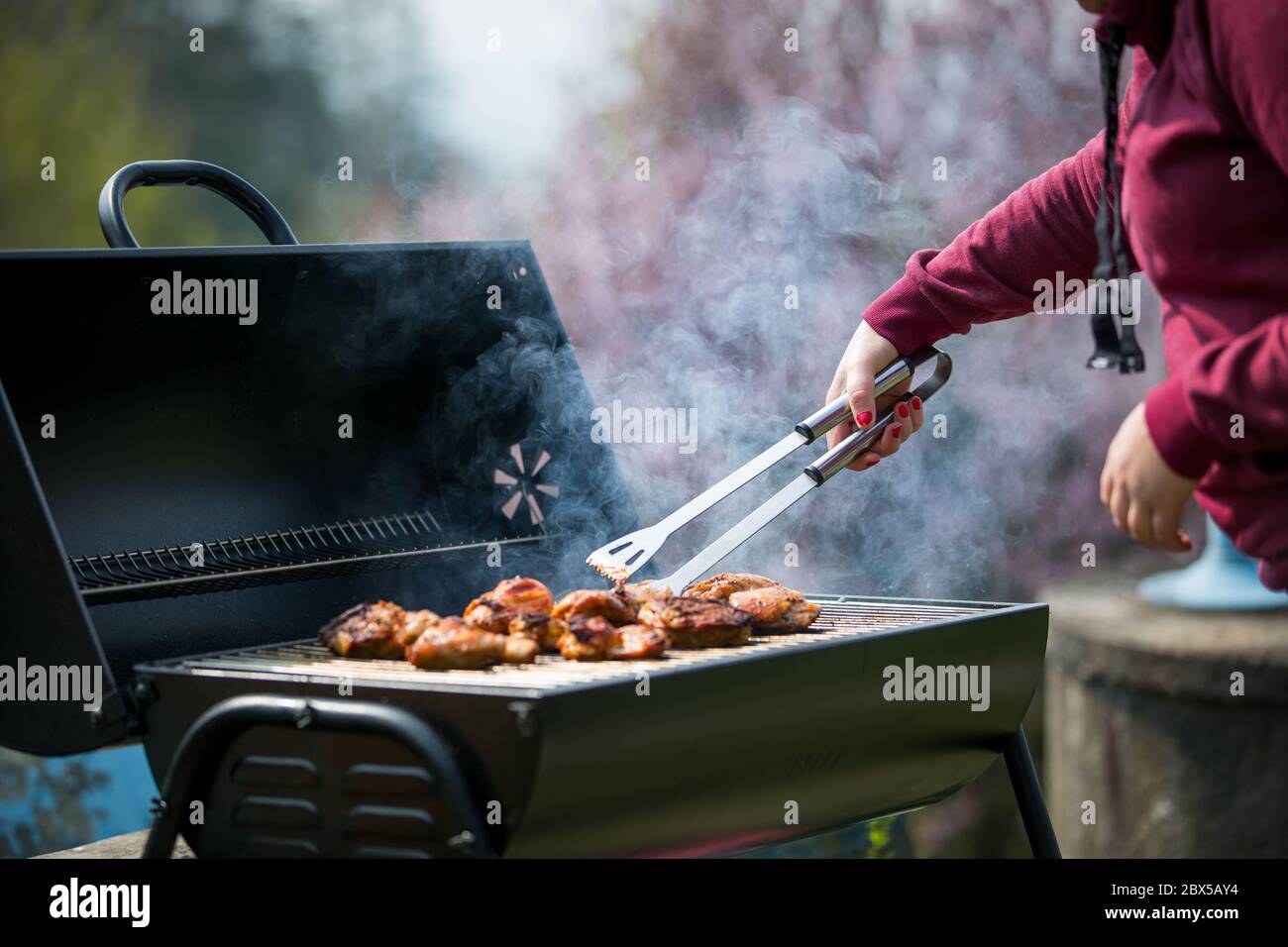 Young woman grills some kind of marinated meat and vegetable on gas ...