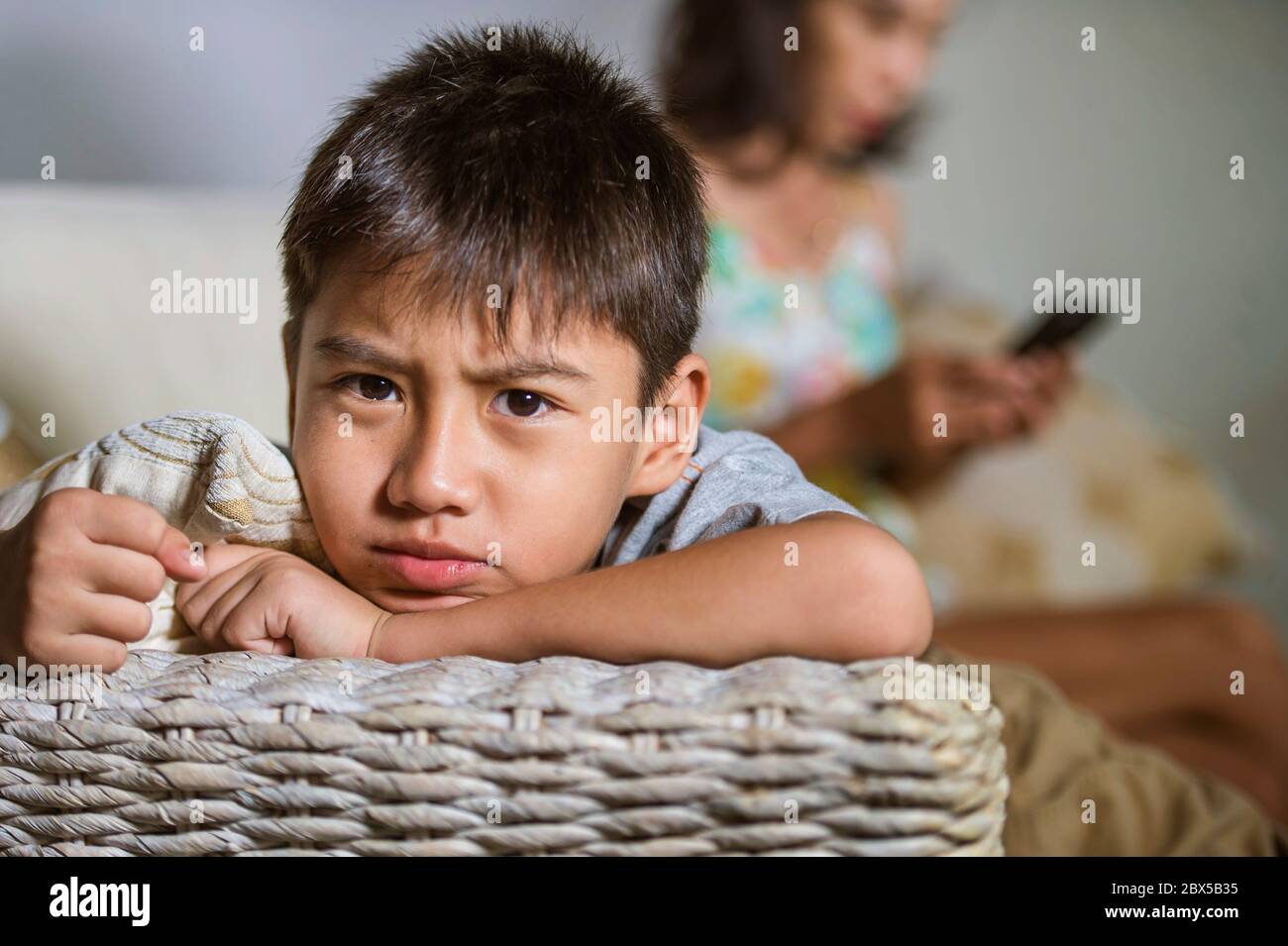 young sad and bored 7 or 8 years old Asian child at home couch feeling ...