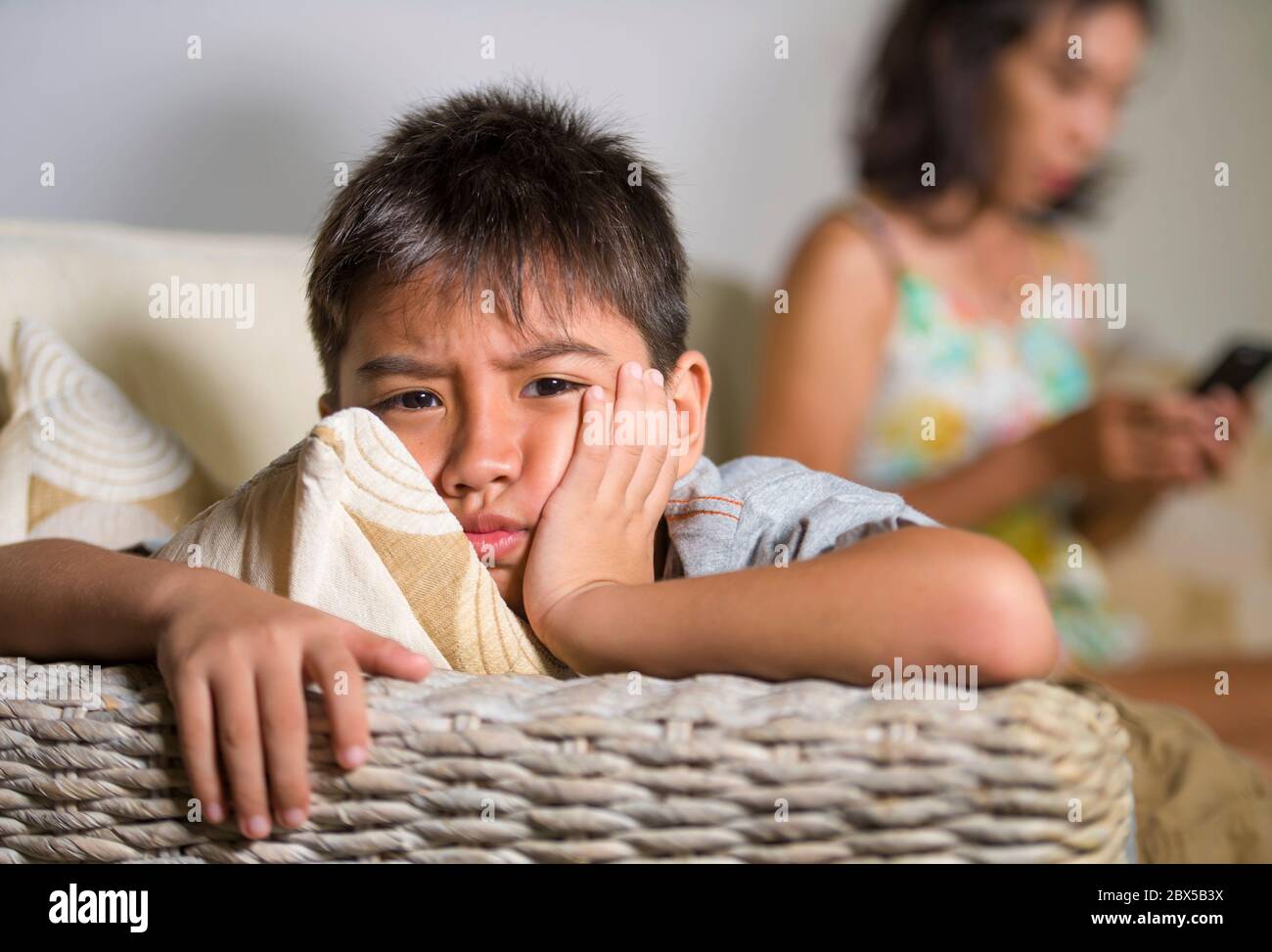 young sad and bored 7 or 8 years old Asian child at home couch feeling ...