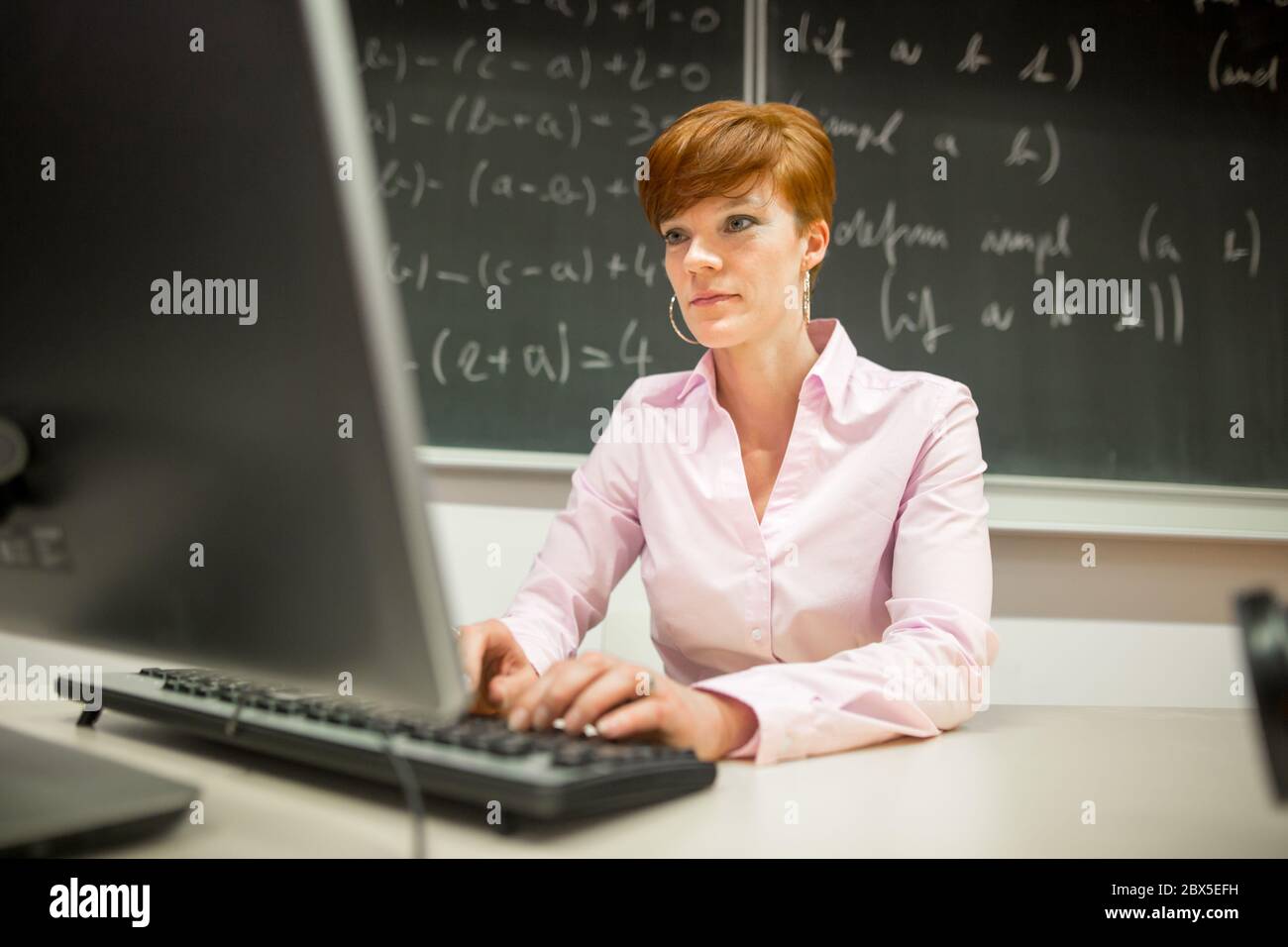 Pretty young college teacher using computer at modern classroom, black ...