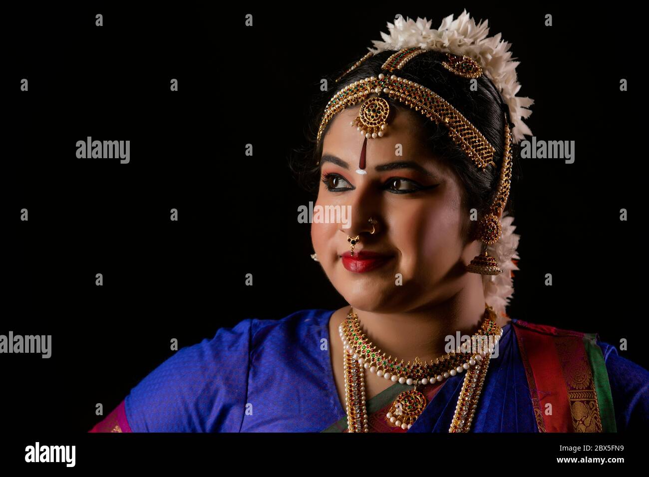 Beautiful bharatnatyam dancer standing in front of a dark background ...