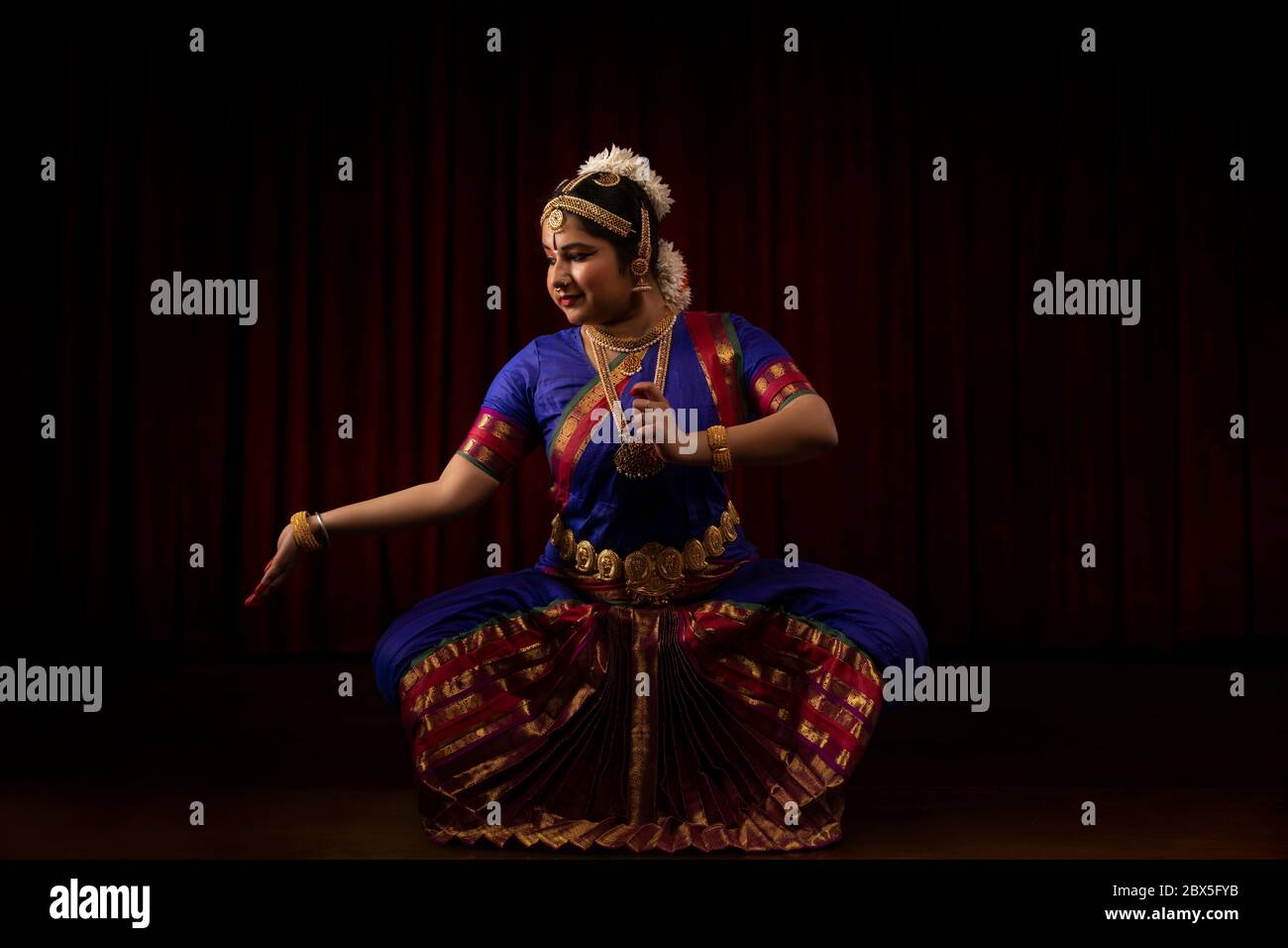 Bharatnatyam dancer sitting in muzhu mandi position in front of a dark ...