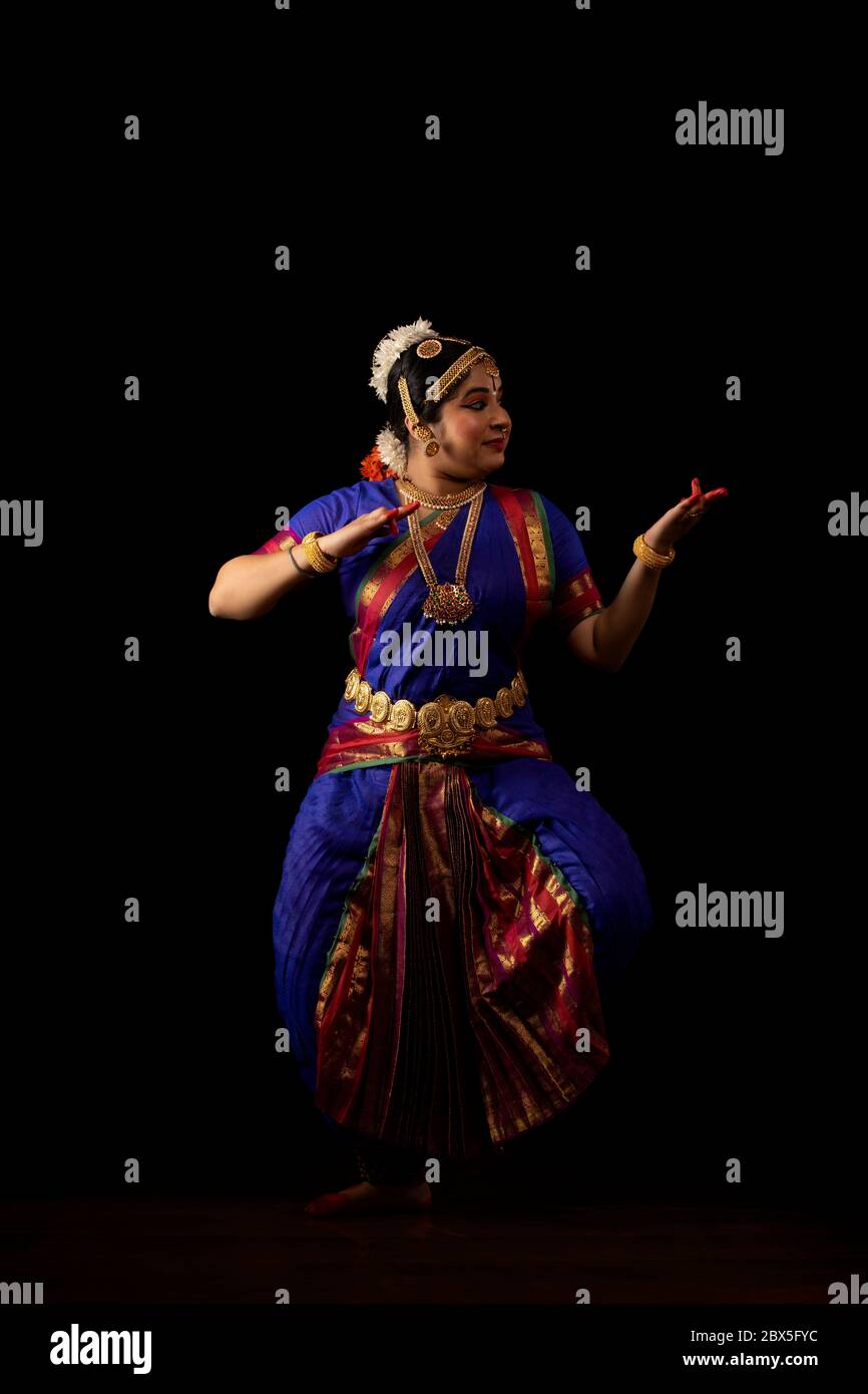 Bharatnatyam dancer standing in araimandi position in front of a dark ...