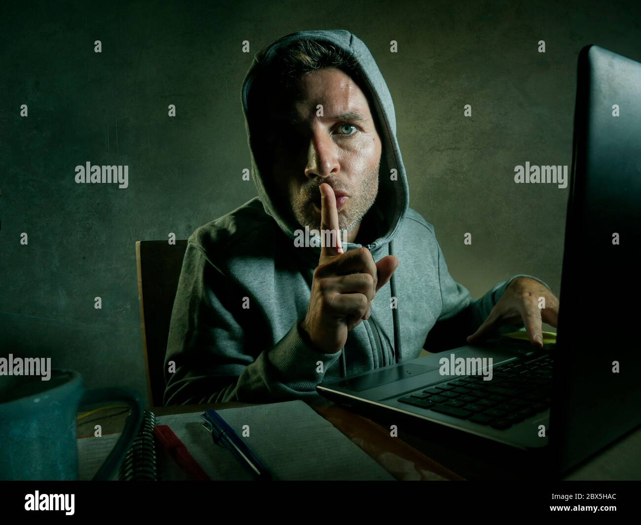 Dangerous Looking Young Hacker Man In Hoodie Typing On Laptop Computer