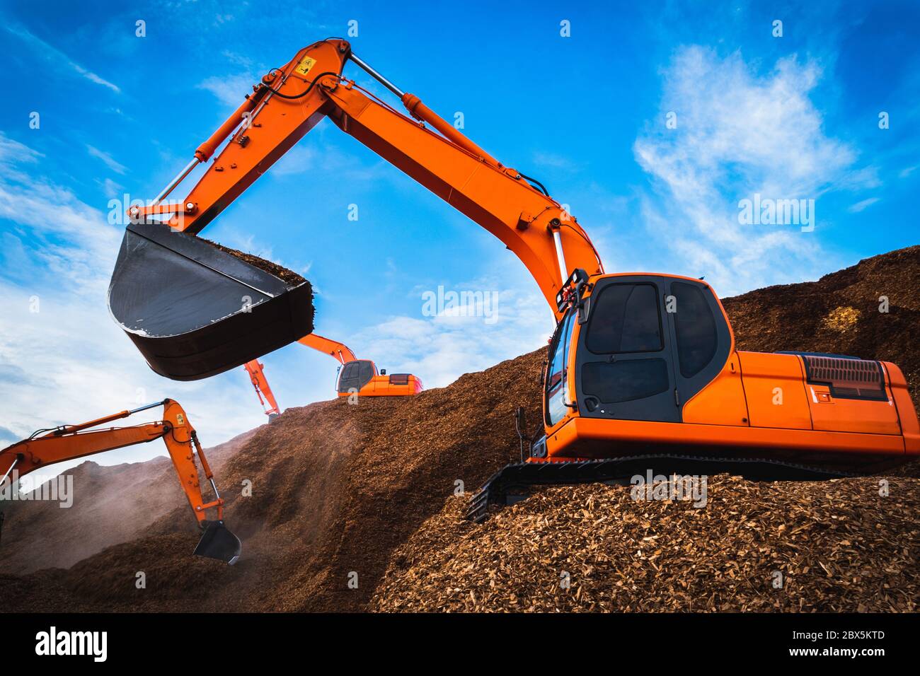 Backhoe standing on big pile of wood chips loading up into truck ...