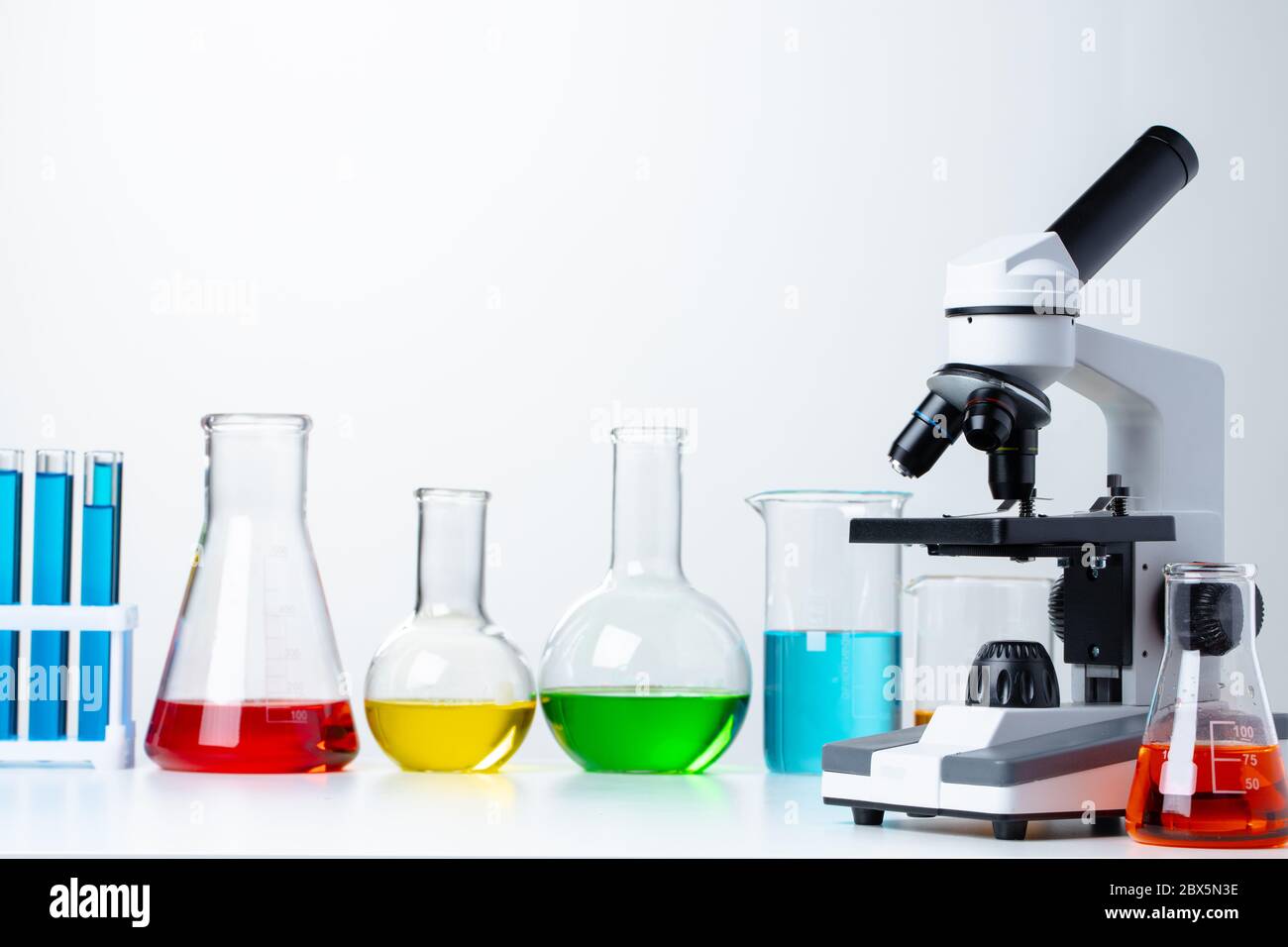Lab microscope with laboratory glassware on desk Stock Photo - Alamy