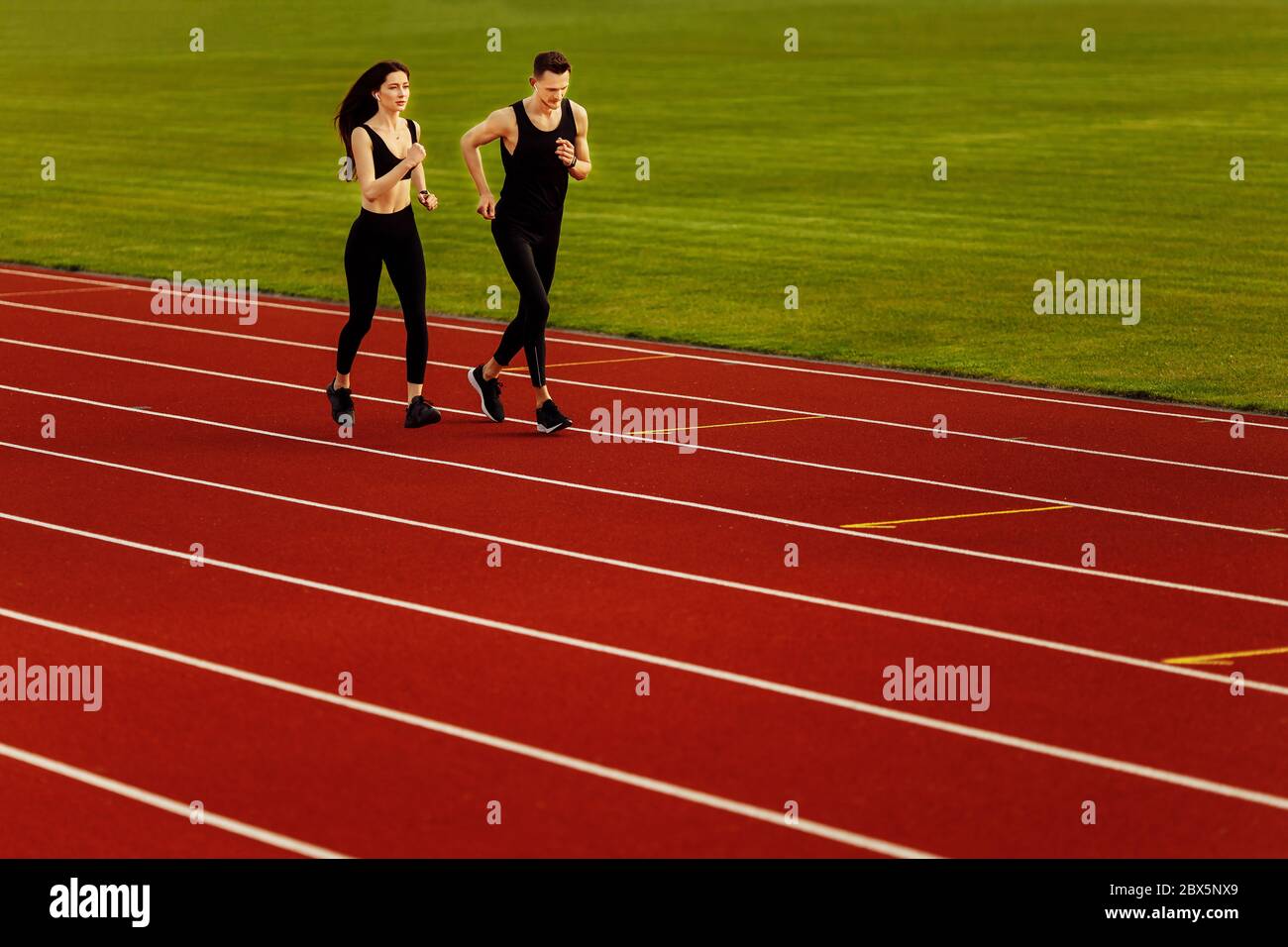 Young man and woman running on race track in modern stadium Stock Photo ...
