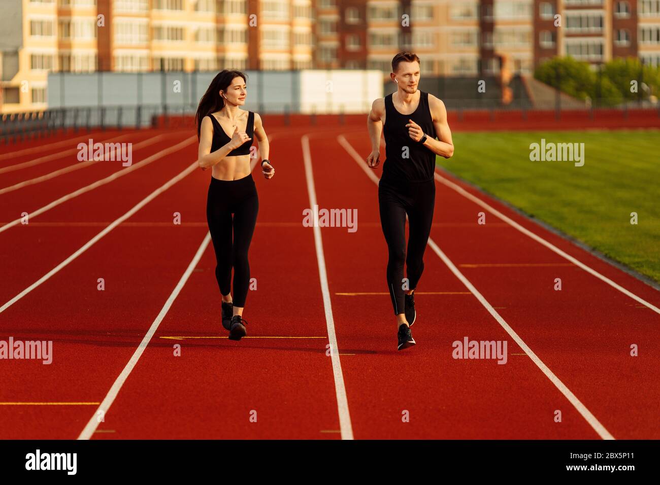 Young man and woman running on race track in modern stadium Stock Photo ...