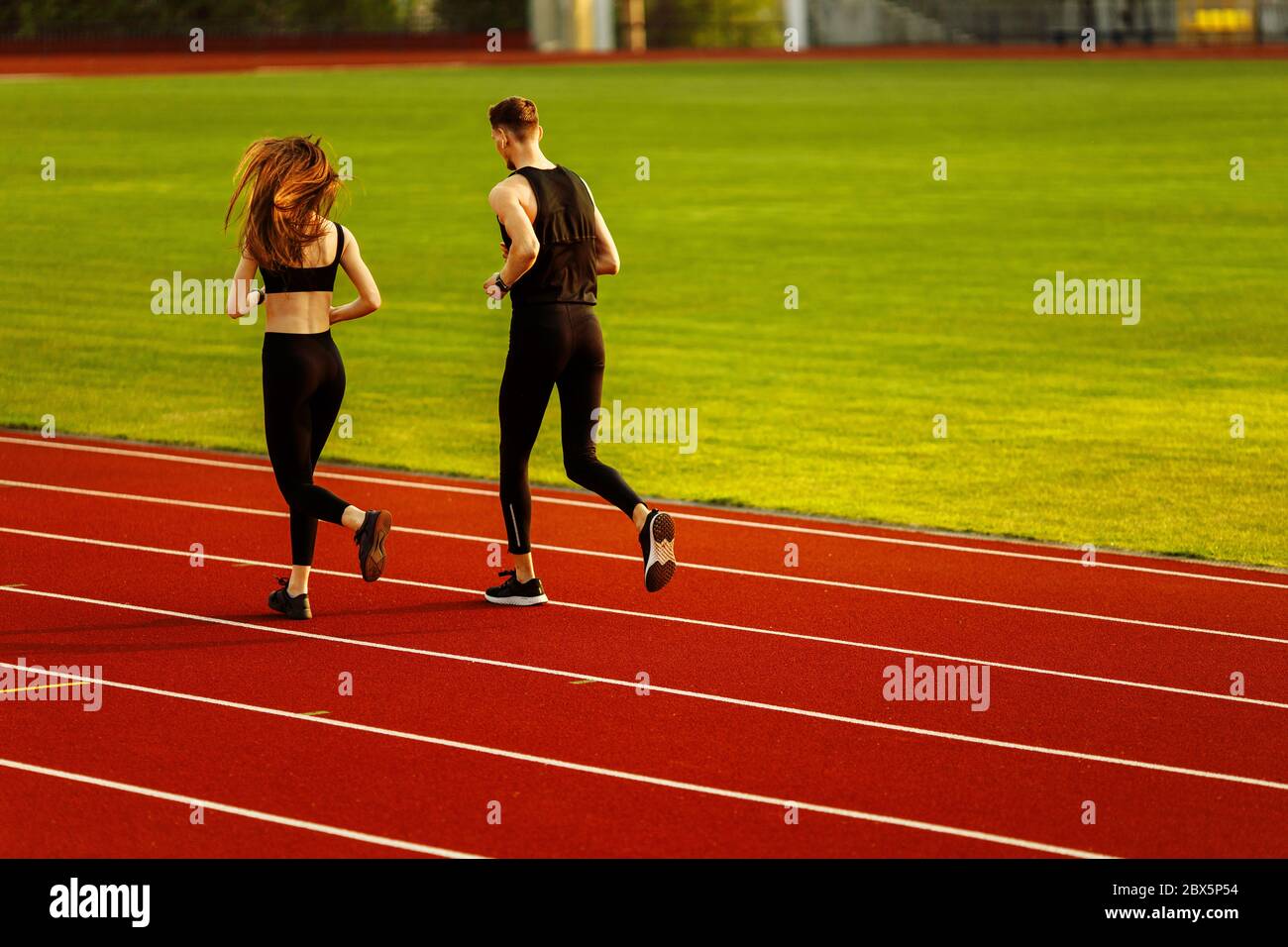 Young man and woman running on race track in modern stadium Stock Photo ...