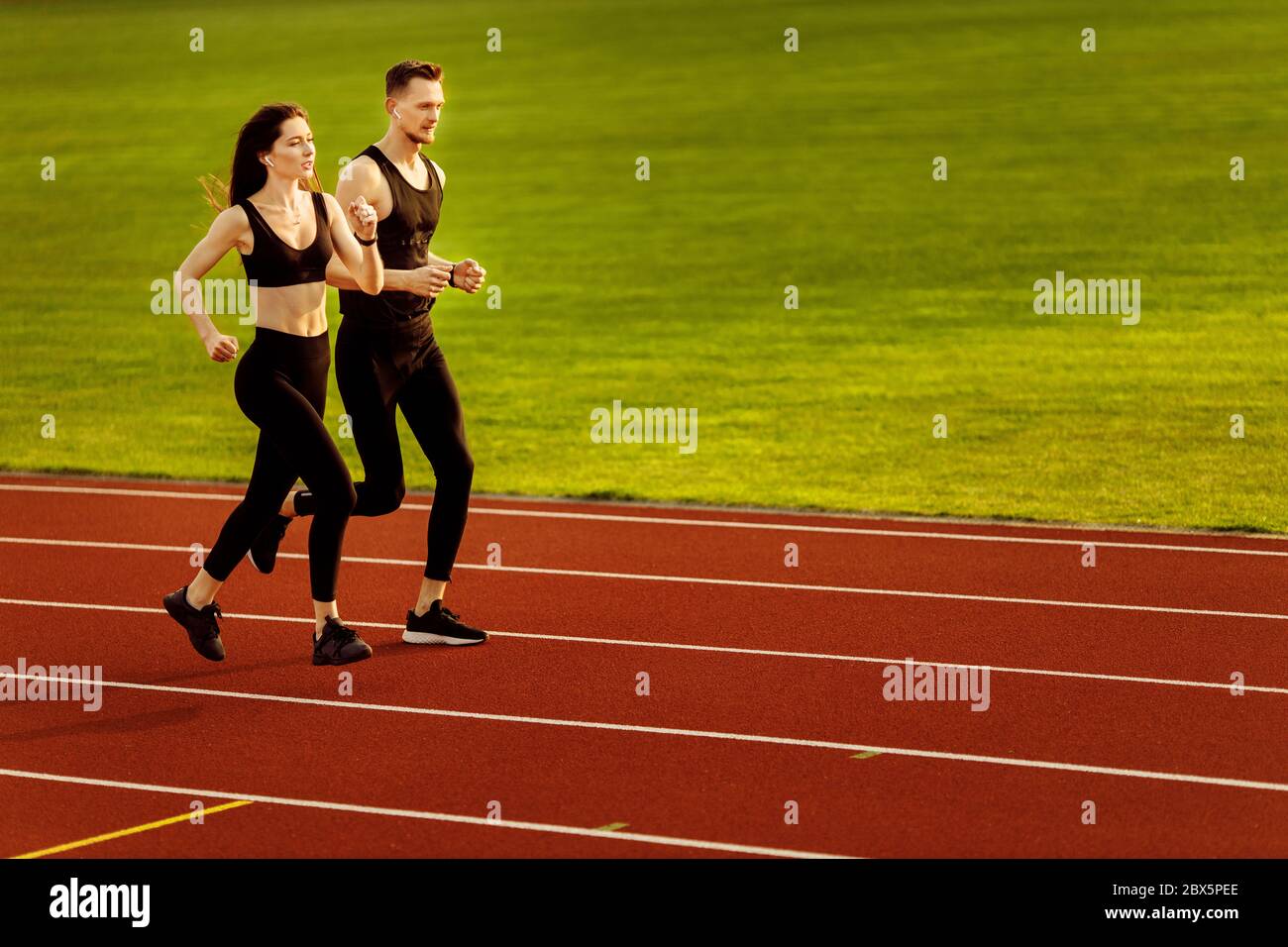 Young man and woman running on race track in modern stadium Stock Photo ...