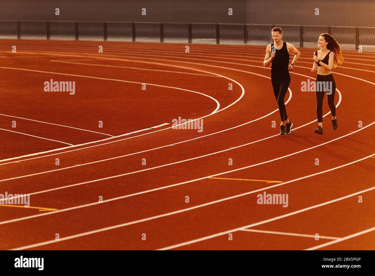 Young man and woman running on race track in modern stadium Stock Photo ...