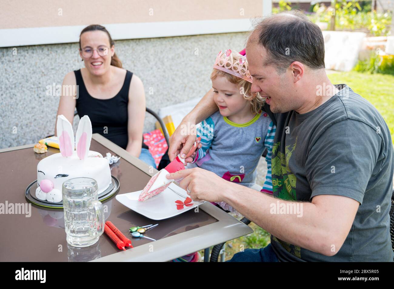Cute blonde girl cutting her birthday cake with parent helping her ...