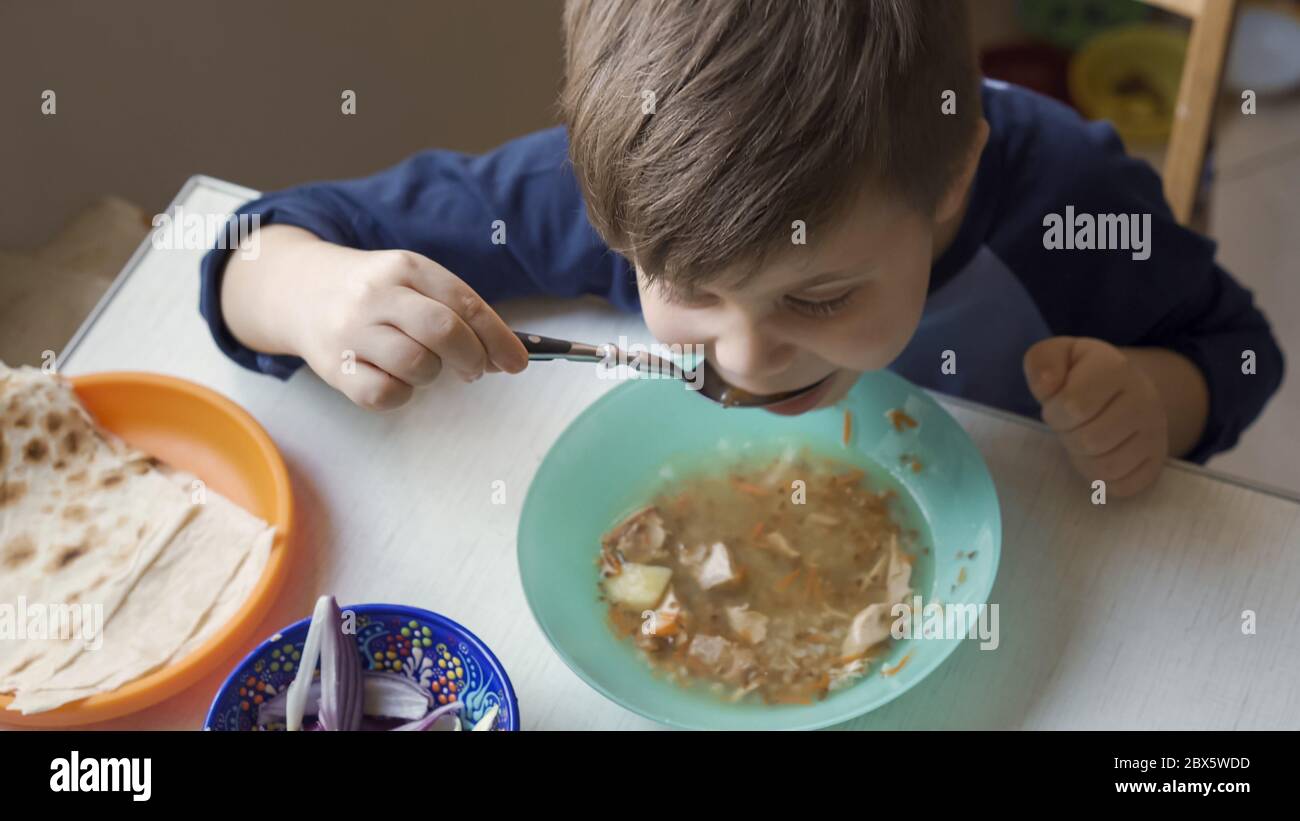 Hungry preschool boy eating soup from a green bowl. Charming Caucasian ...