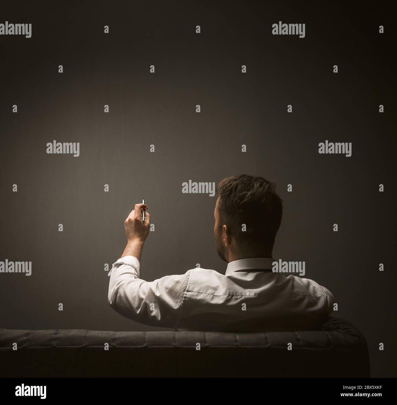 Businessman writing with pen on dark gray wall. View from the back of ...