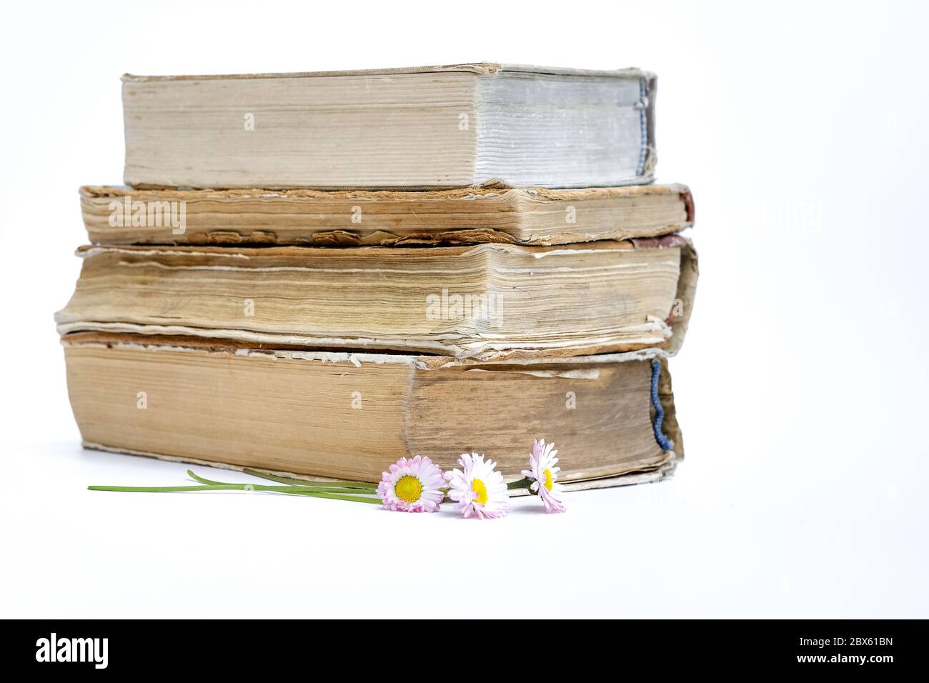 a stack of old books. bouquet of flowers from daisies on a white ...