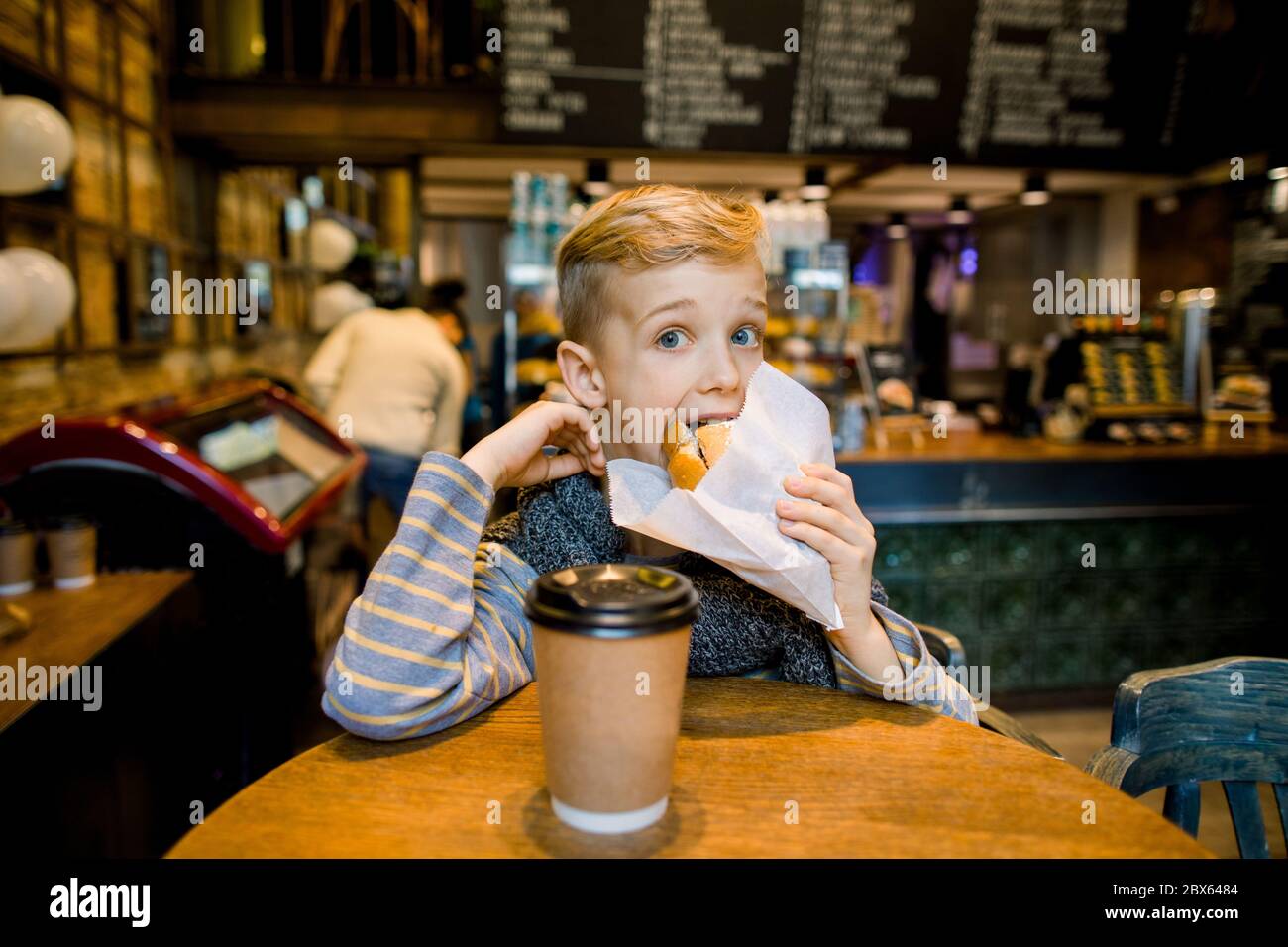 Happy cute boy eating fresh croissant, sitting at the table in city ...