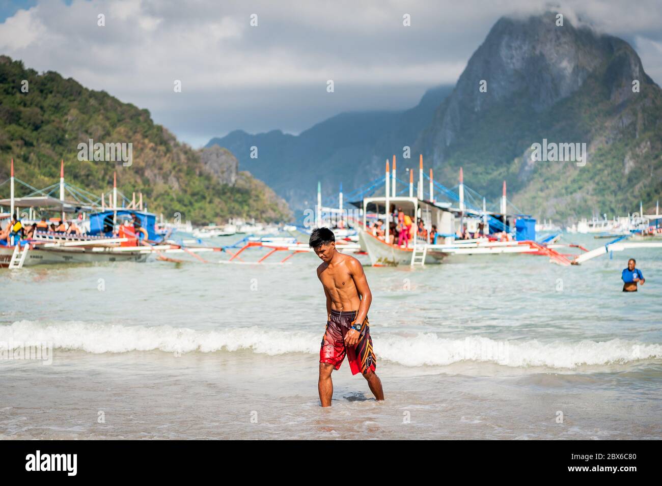 El Nido filipino boat hands wade into shore from the numerous boats ...