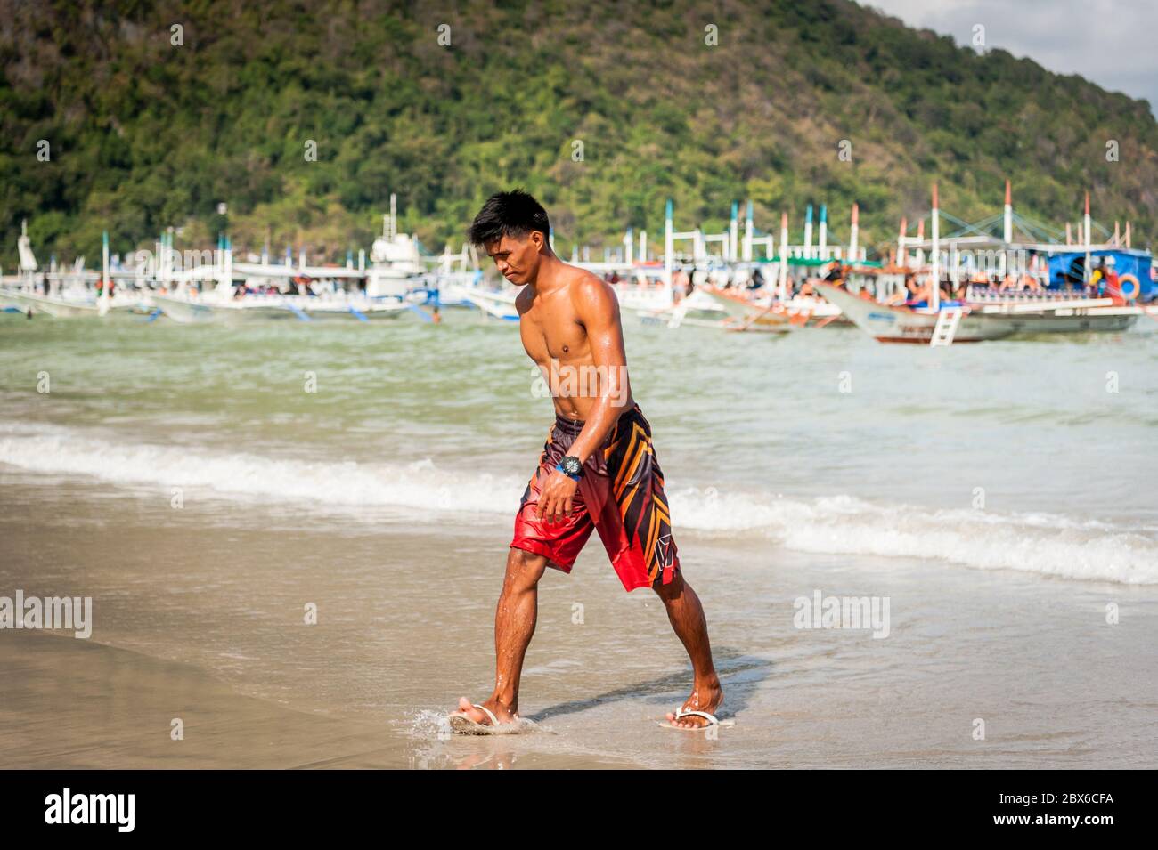 El Nido filipino boat hands wade into shore from the numerous boats ...