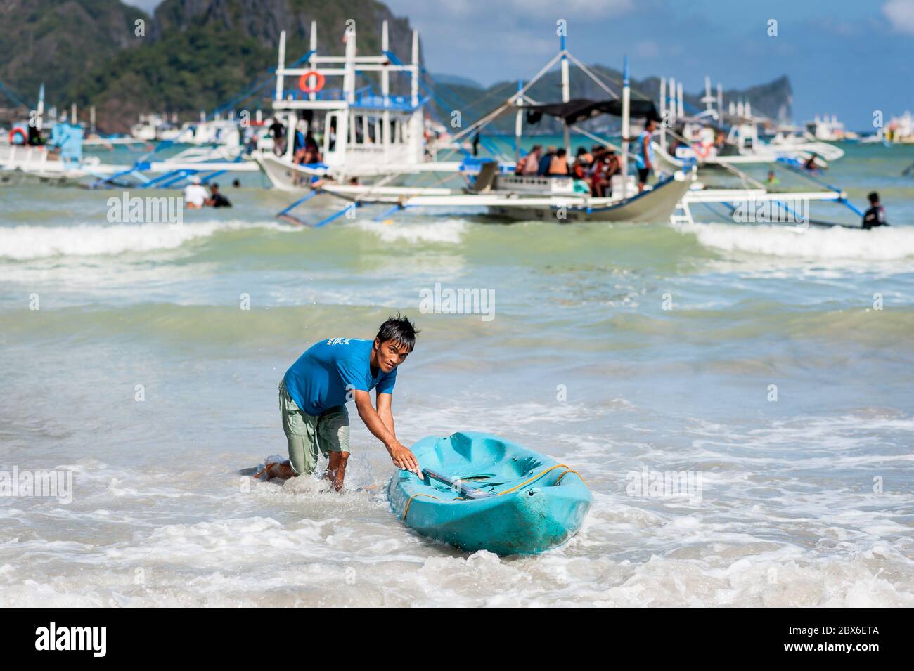 El Nido filipino boat hands wade into shore from the numerous boats ...