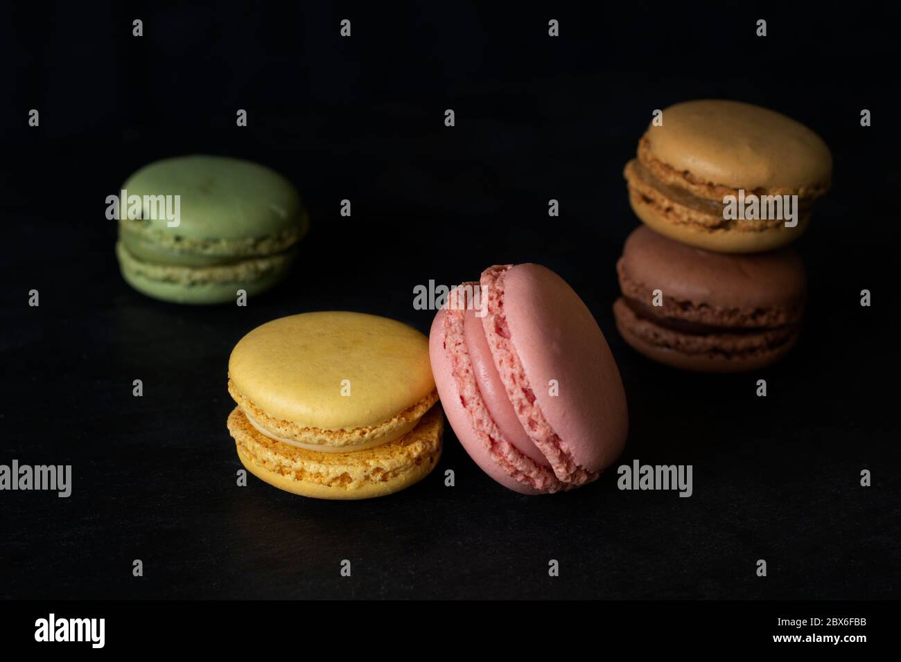 Five colored macarons on a black background, with low key lighting ...