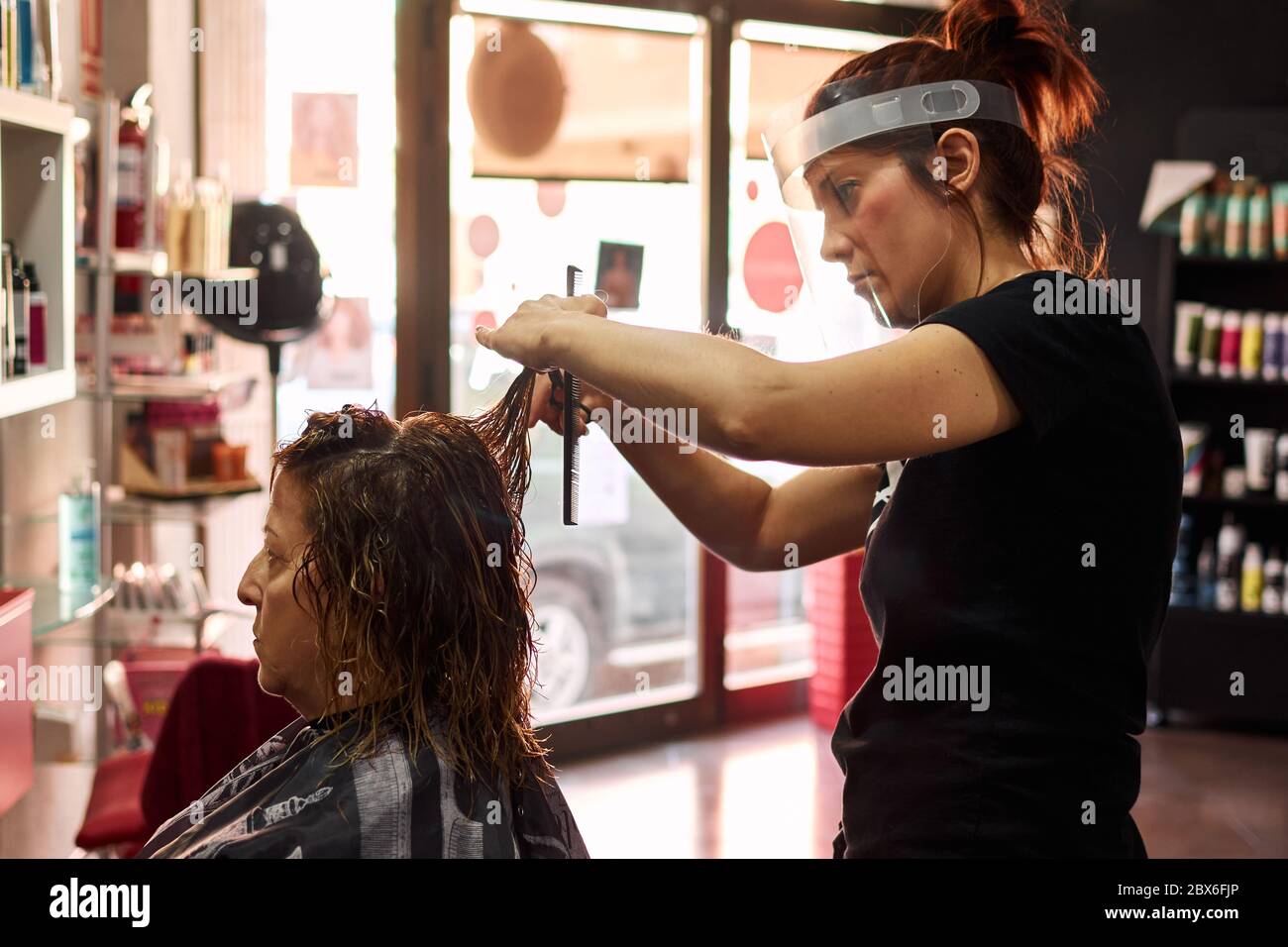 Hairdresser cuts a client's hair with a face shield Stock Photo - Alamy