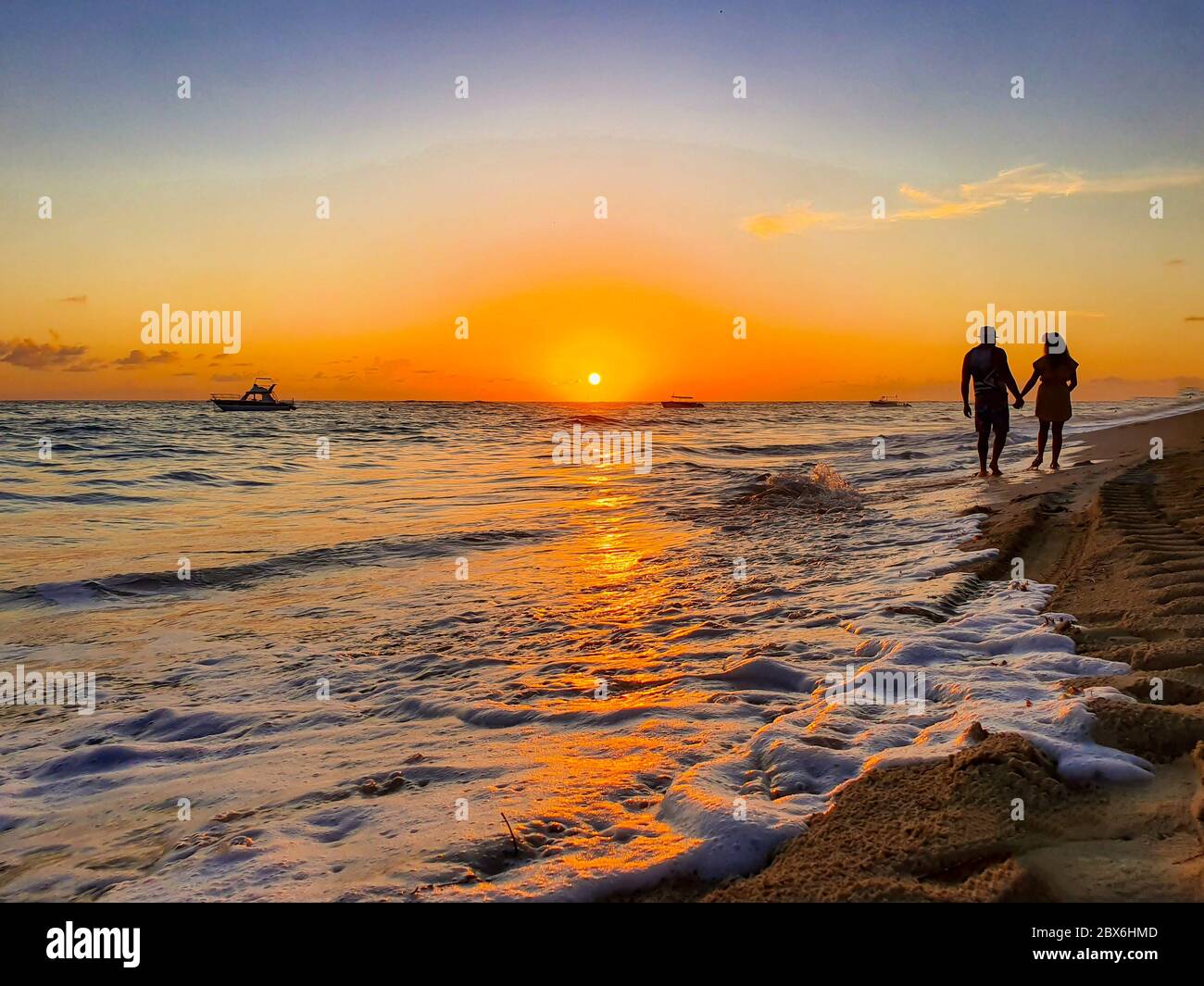 Couple's silhouette on the beach at sunset with boat in the background ...
