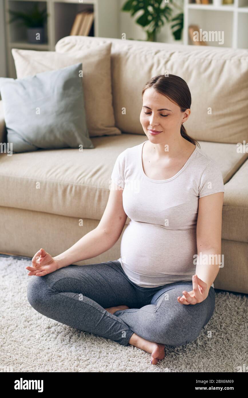 Young positive pregnant woman in activewear sitting in pose of lotus by ...