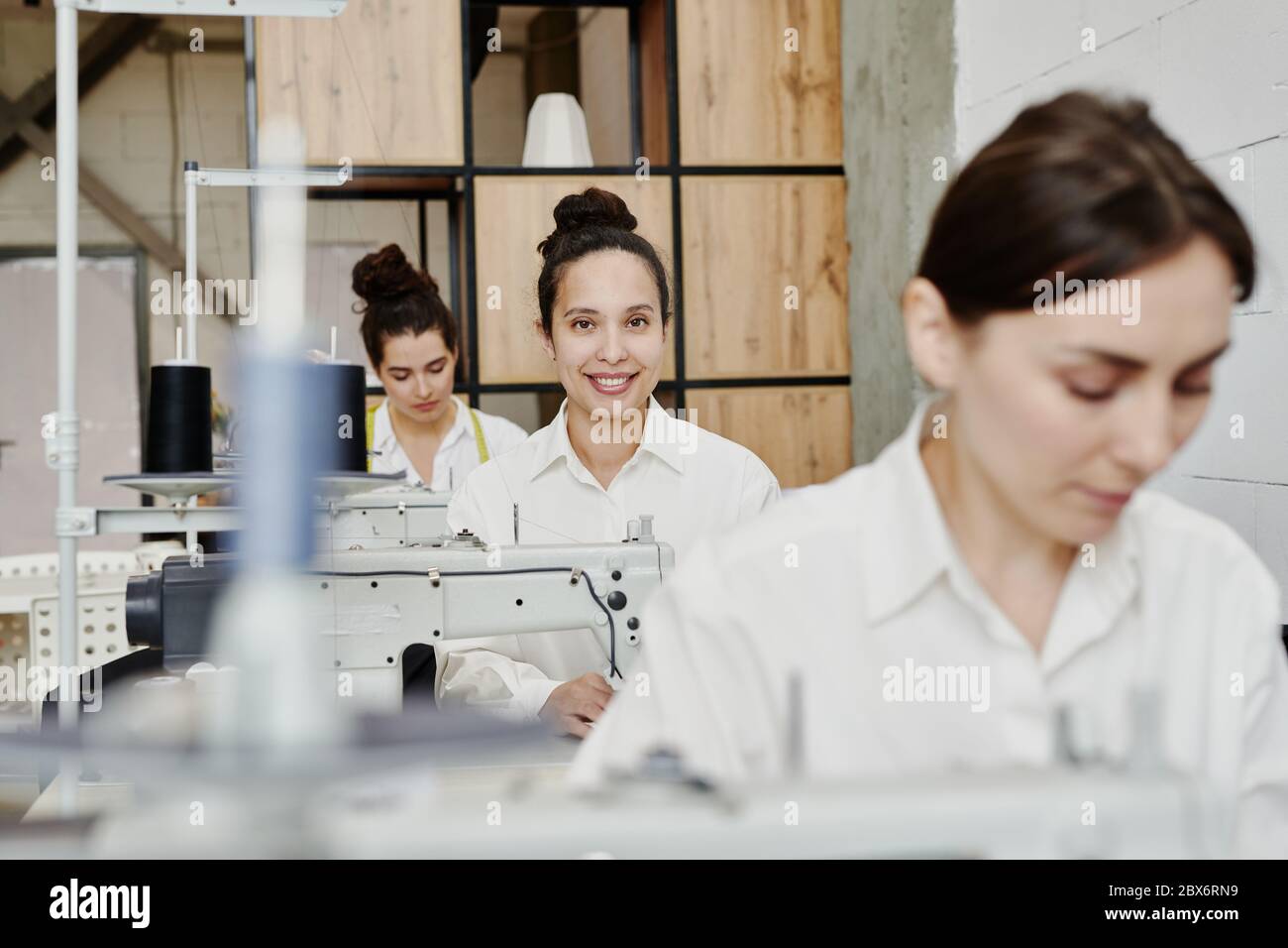 Happy young seamstress with toothy smile looking at you among her ...