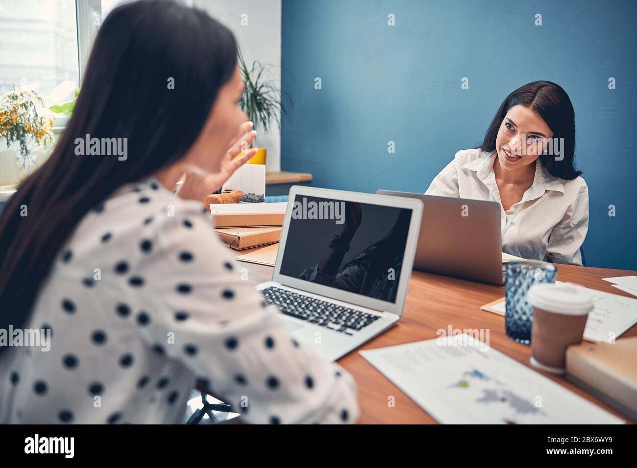 Pretty ladies sitting in office while talking Stock Photo - Alamy