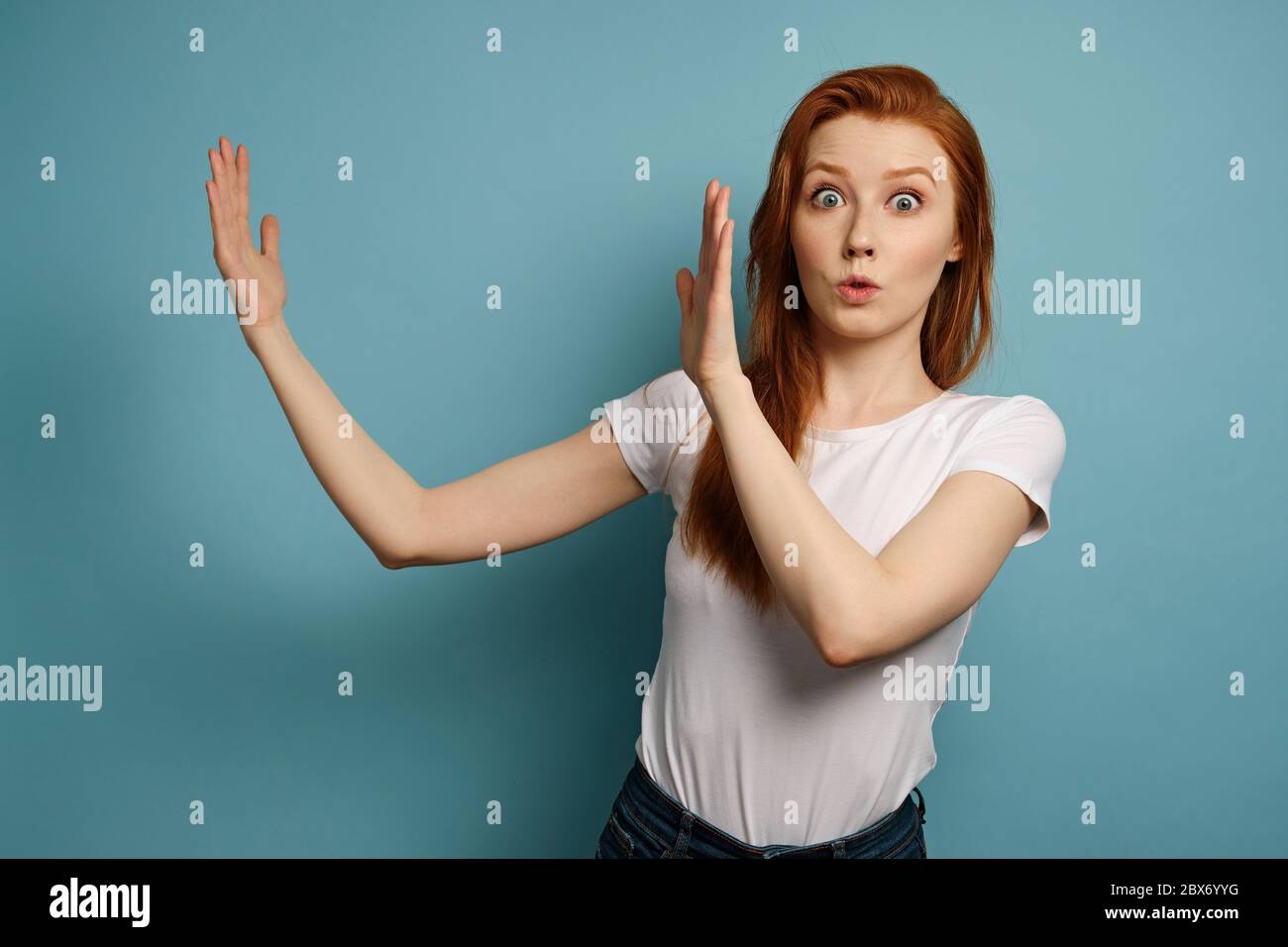 A red-haired girl in a white T-shirt stands and shows with hands a ...