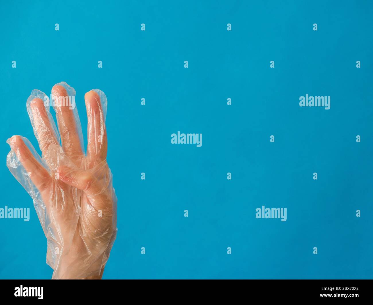Hand with plastic glove with four fingers up on blue background with ...