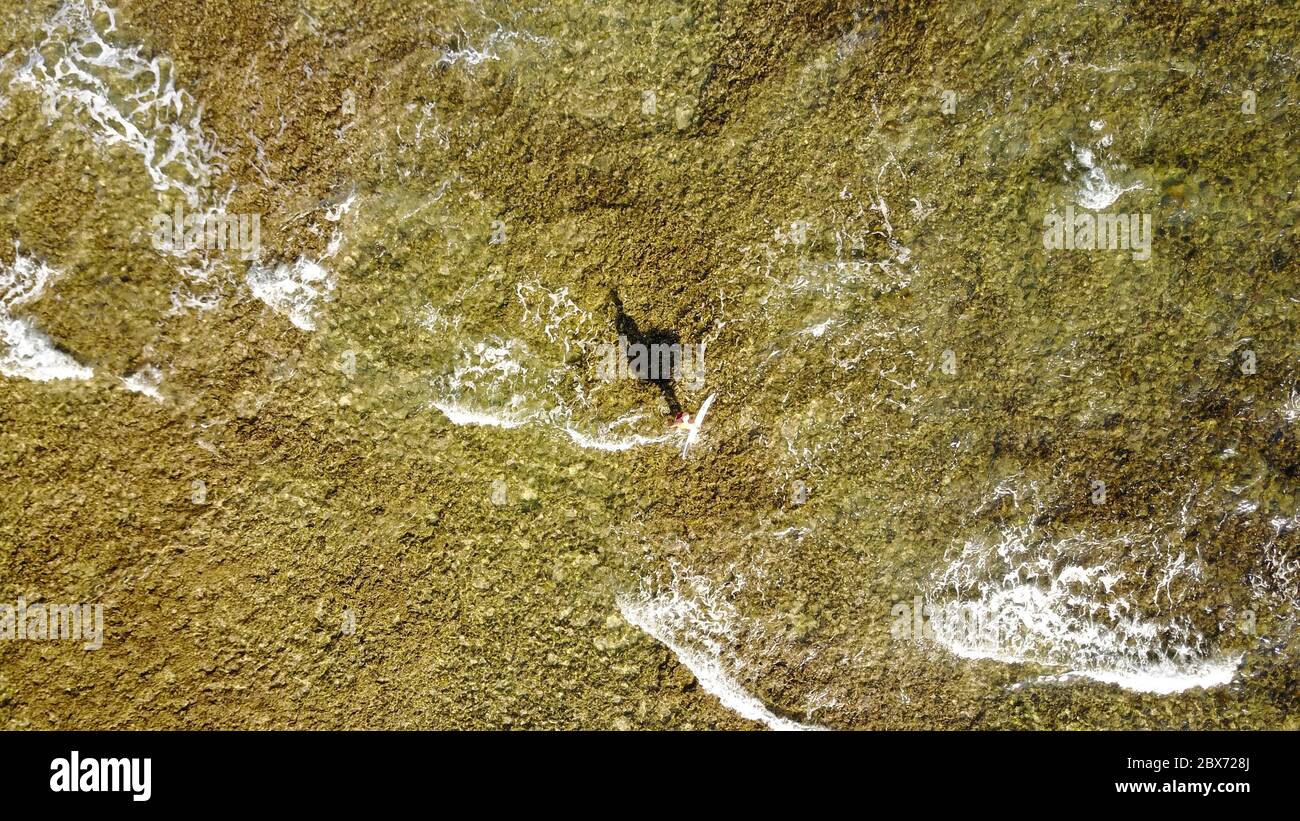 Aerial view of the surfer holding a surfing board and approaching the ...