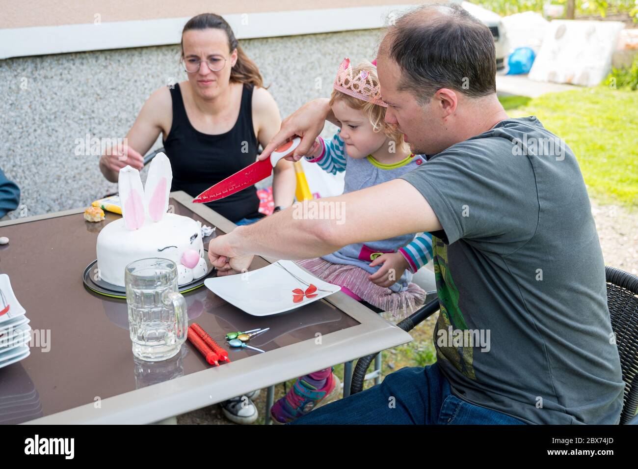 Cute blonde girl cutting her birthday cake with parent helping her ...