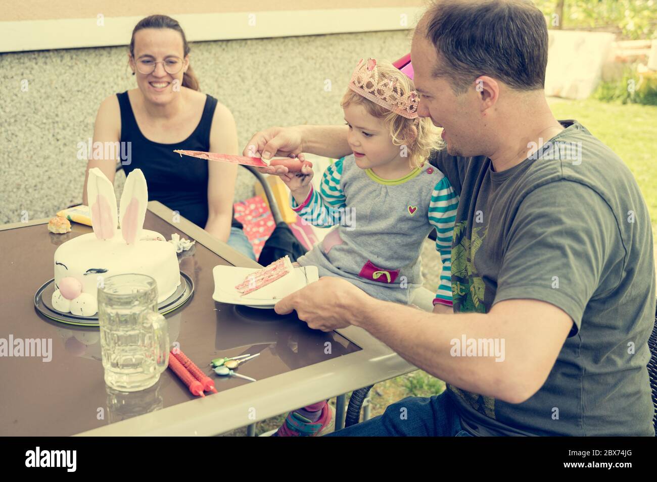 Cute blonde girl cutting her birthday cake with parent helping her ...