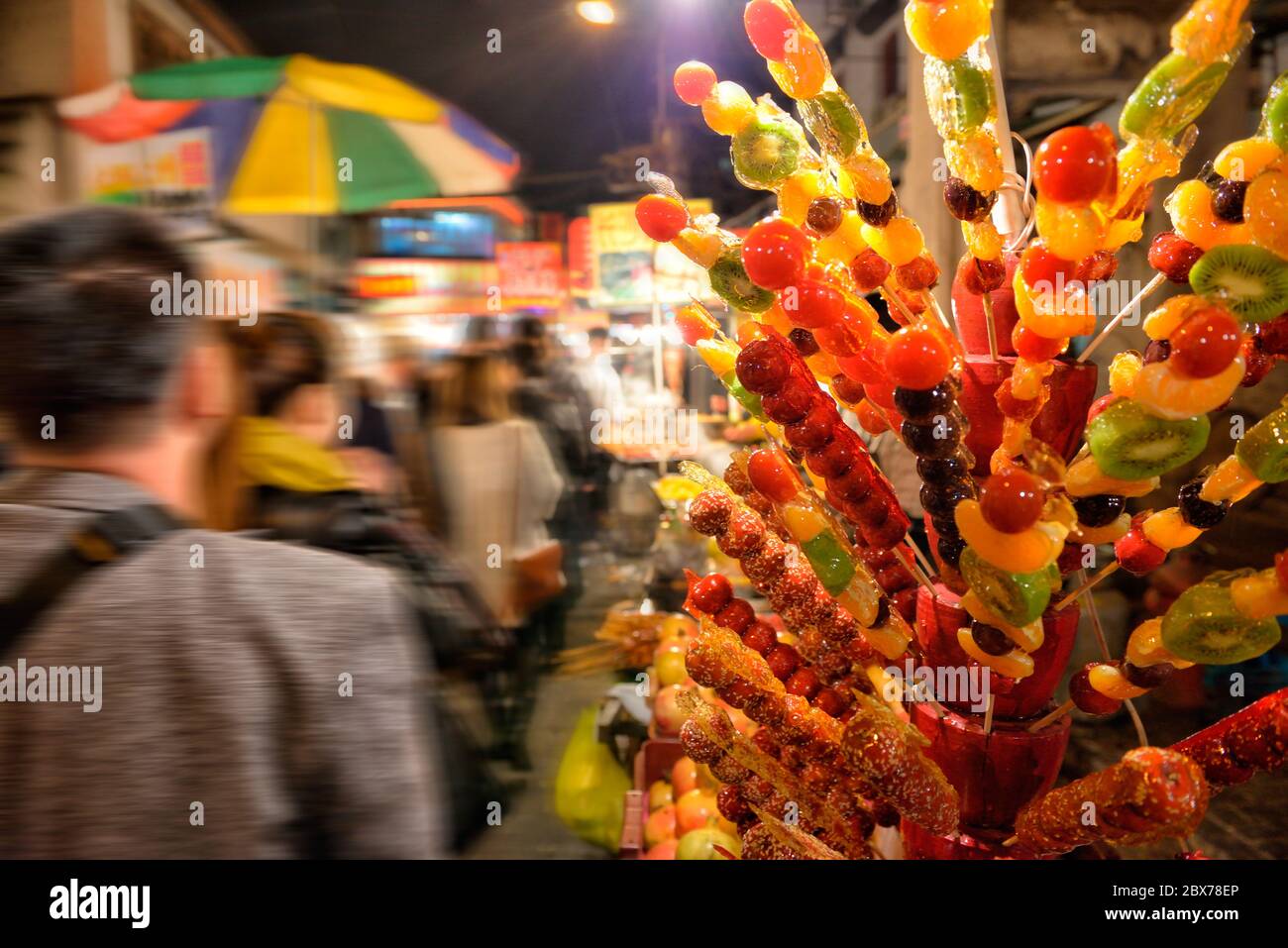 Assortment of colorful sweet food in the middle of crowd at night fair ...