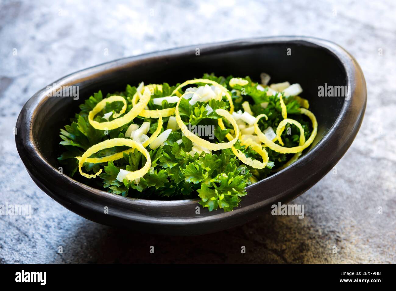 Gremolata ingredients in rustic black dish. Parsley, lemon zest and ...