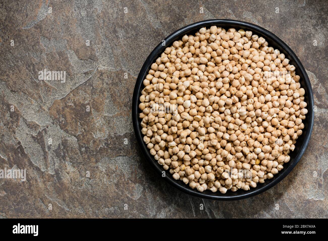 Uncooked chickpeas in rustic black bowl over rough stone background ...