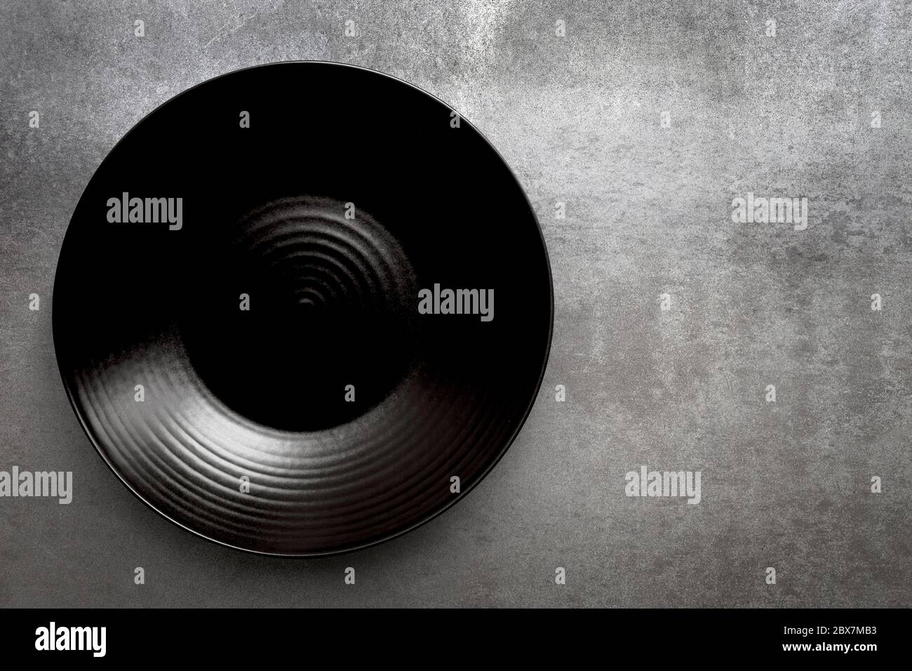 Empty round black plate over gray slate. Aerial view, with copy space ...