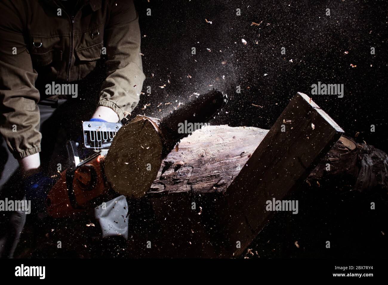 Photo of a worker in outfit with blue gloves cutting wood log on black ...