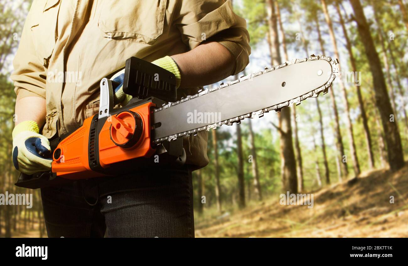 Angle view photo of a worker in outfit standning with chainsaw on ...