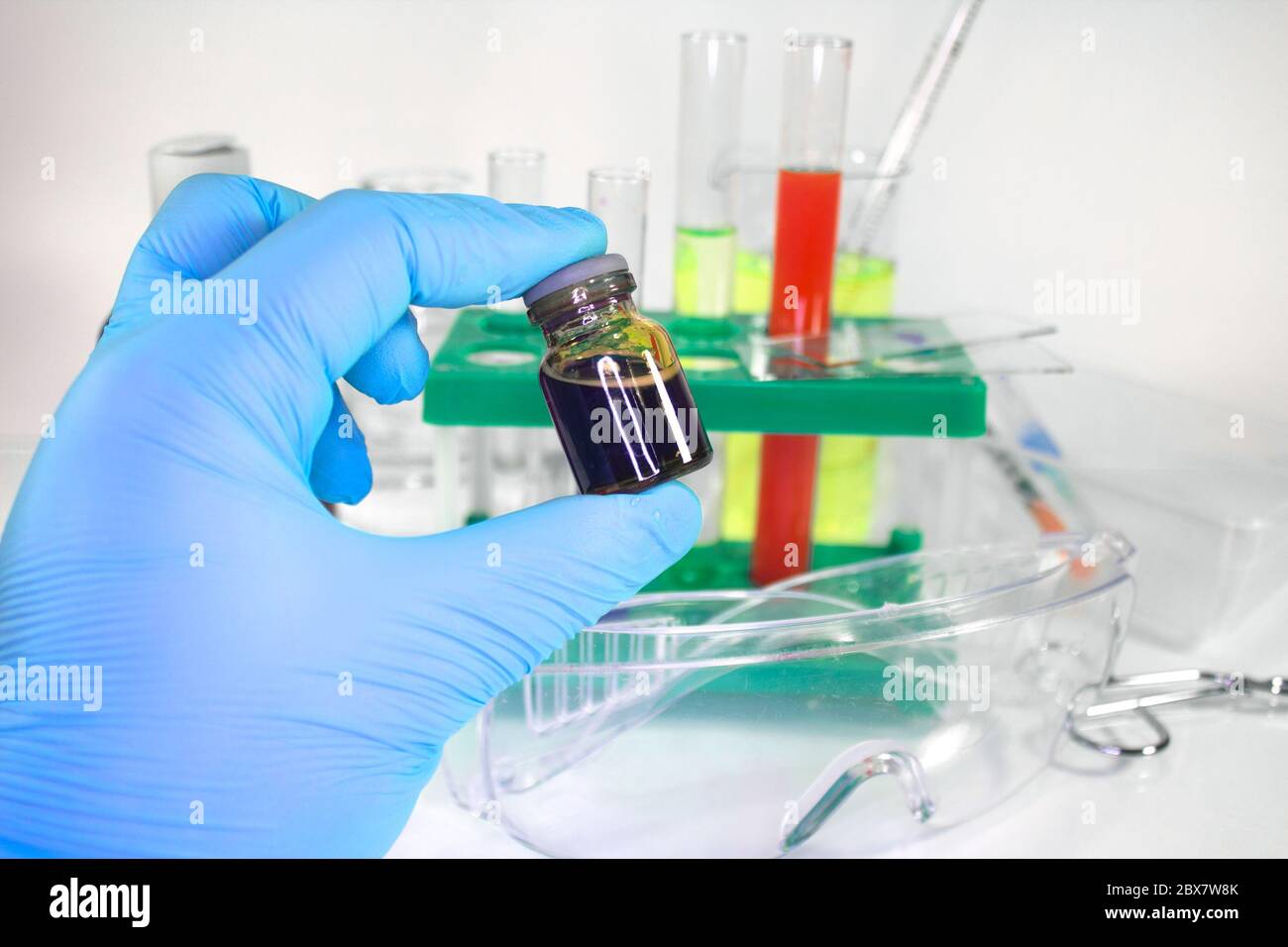 Medical hand in gloves holding a bottle with black liquid on laboratory ...
