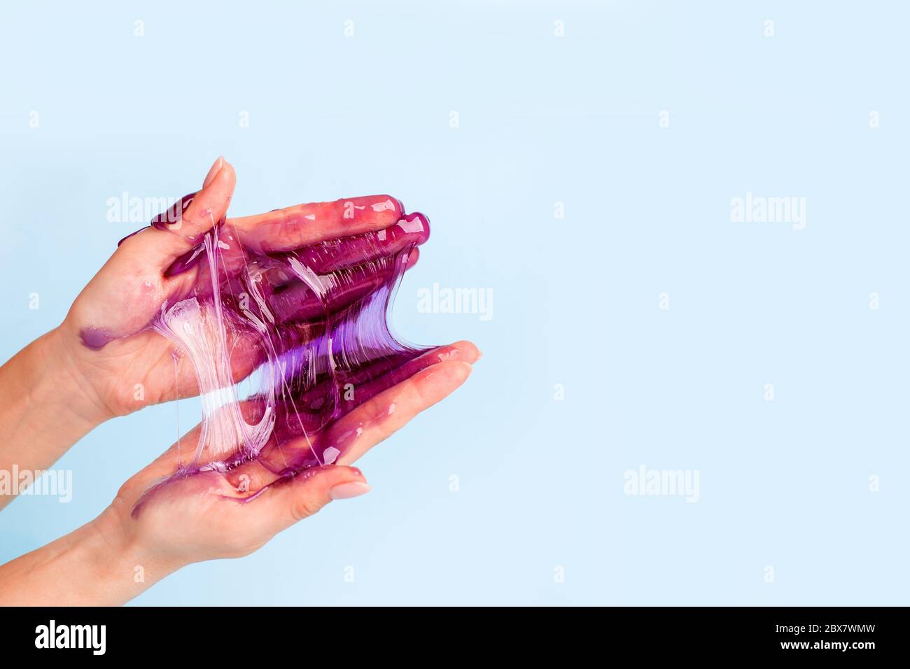Young girl hands with sticky purple slime on blue background, liquid ...