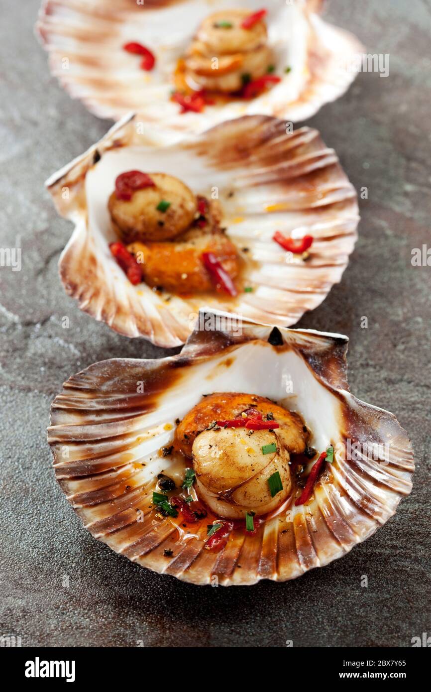 Grilled scallops in scallop shells, with chili. Focus on front scallop ...