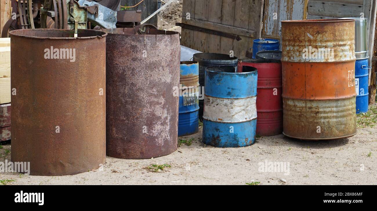 Rusty iron barrels stand on the ground near a village fence panorama ...